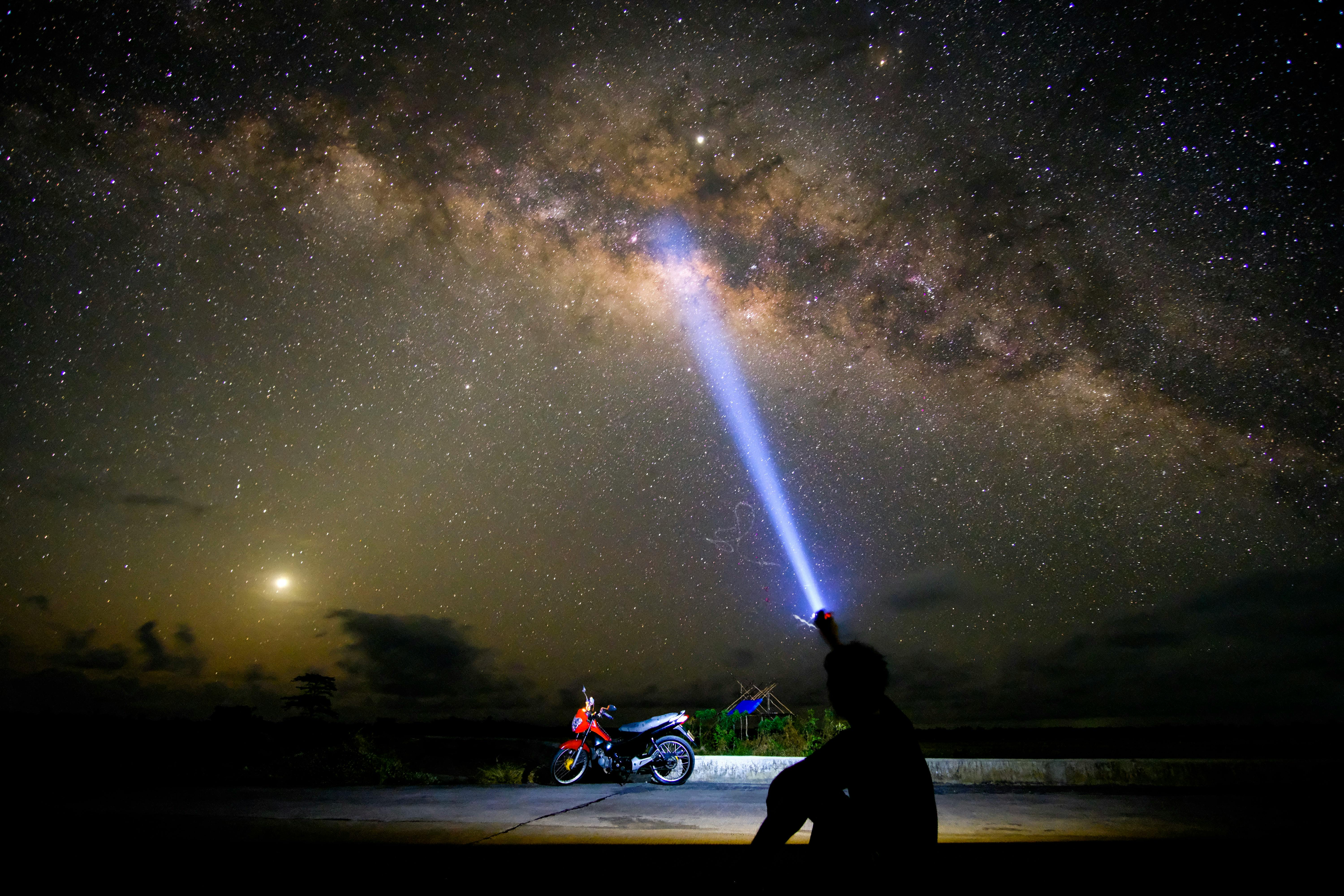 Silhouette of a Person Sitting on the Road Holding a Flashlight during ...