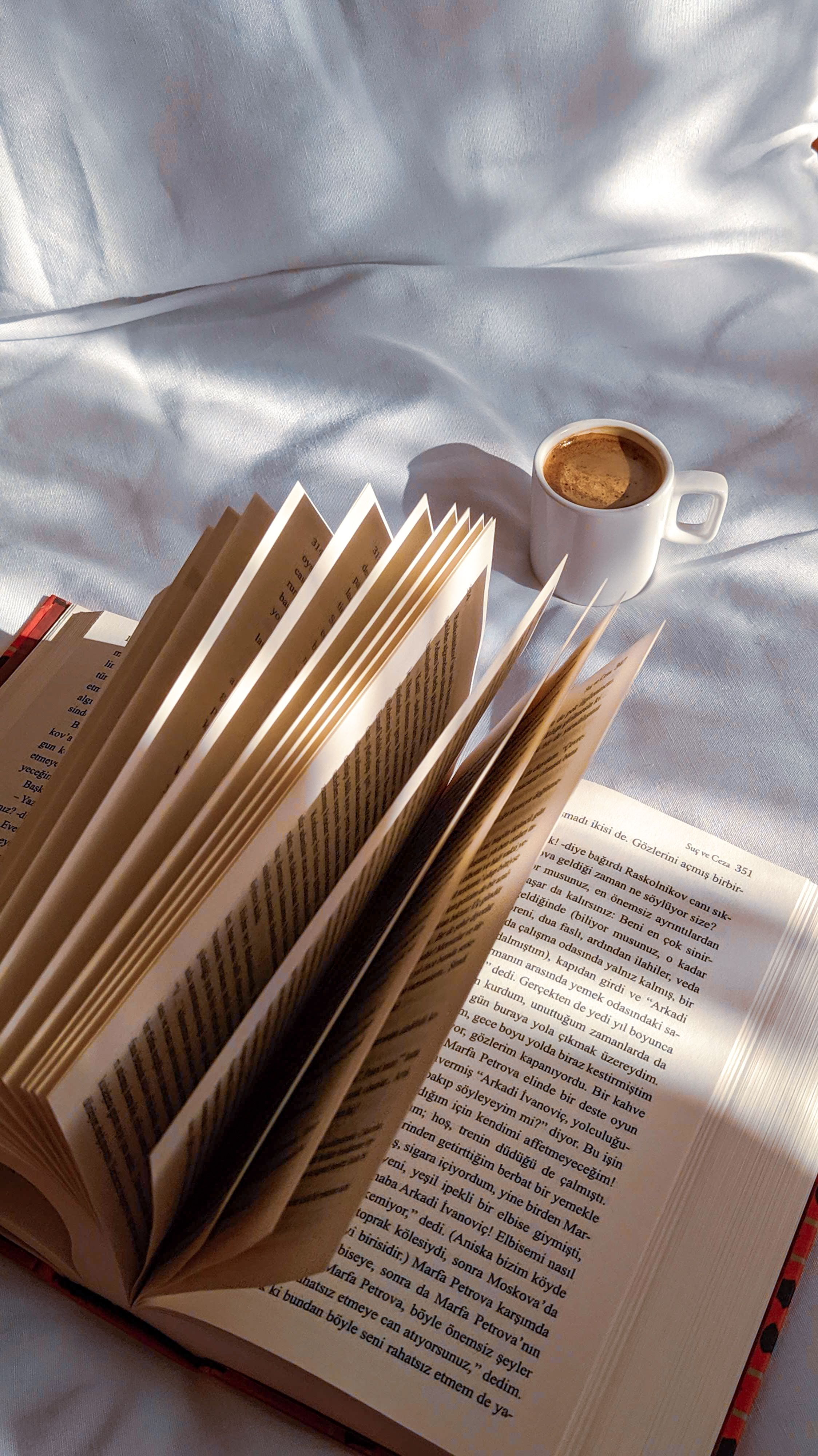 White Ceramic Mug Near an Open Book on White Textile · Free Stock Photo