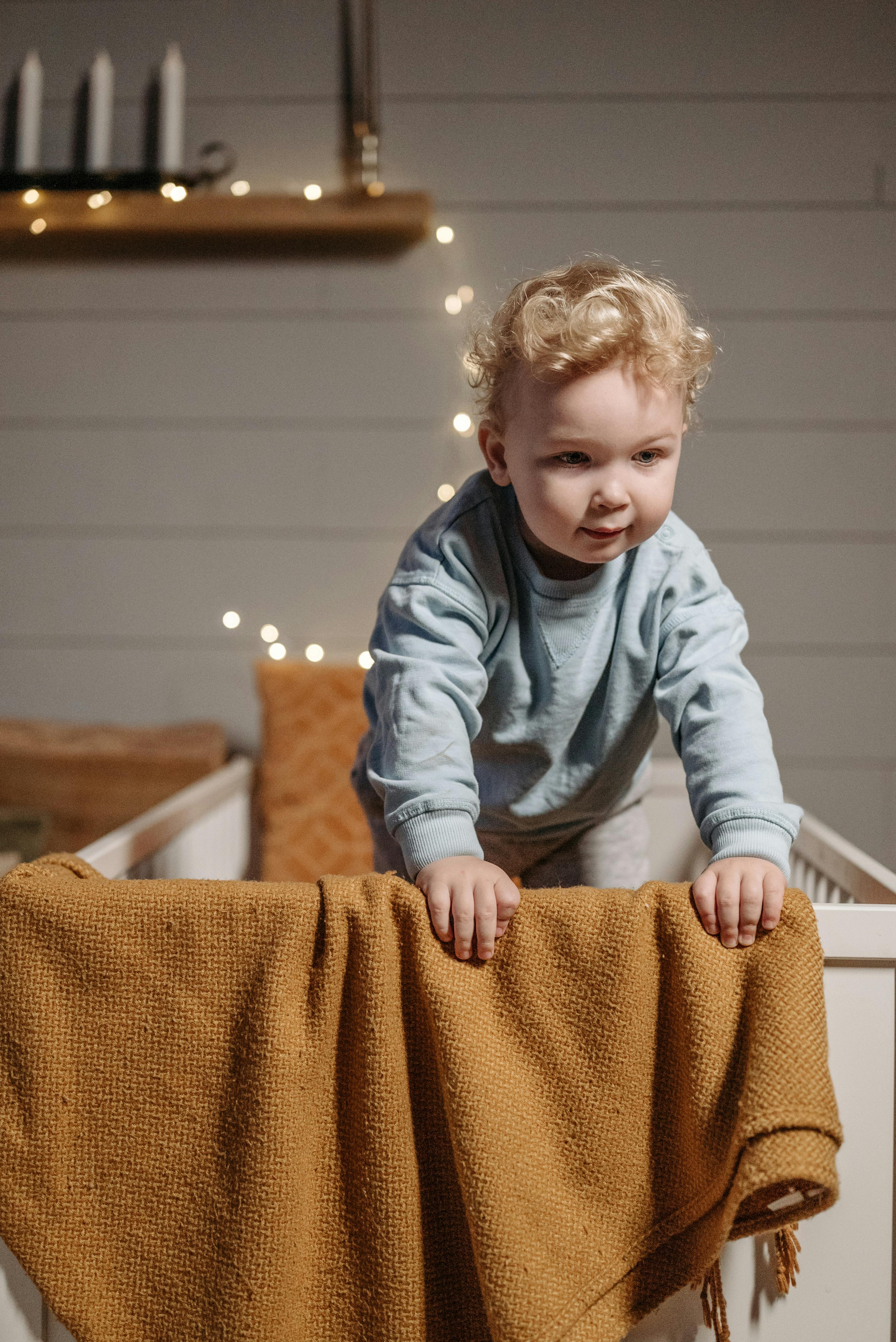 A Cute Baby in Light Blue Sweater Standing at the Crib · Free Stock Photo