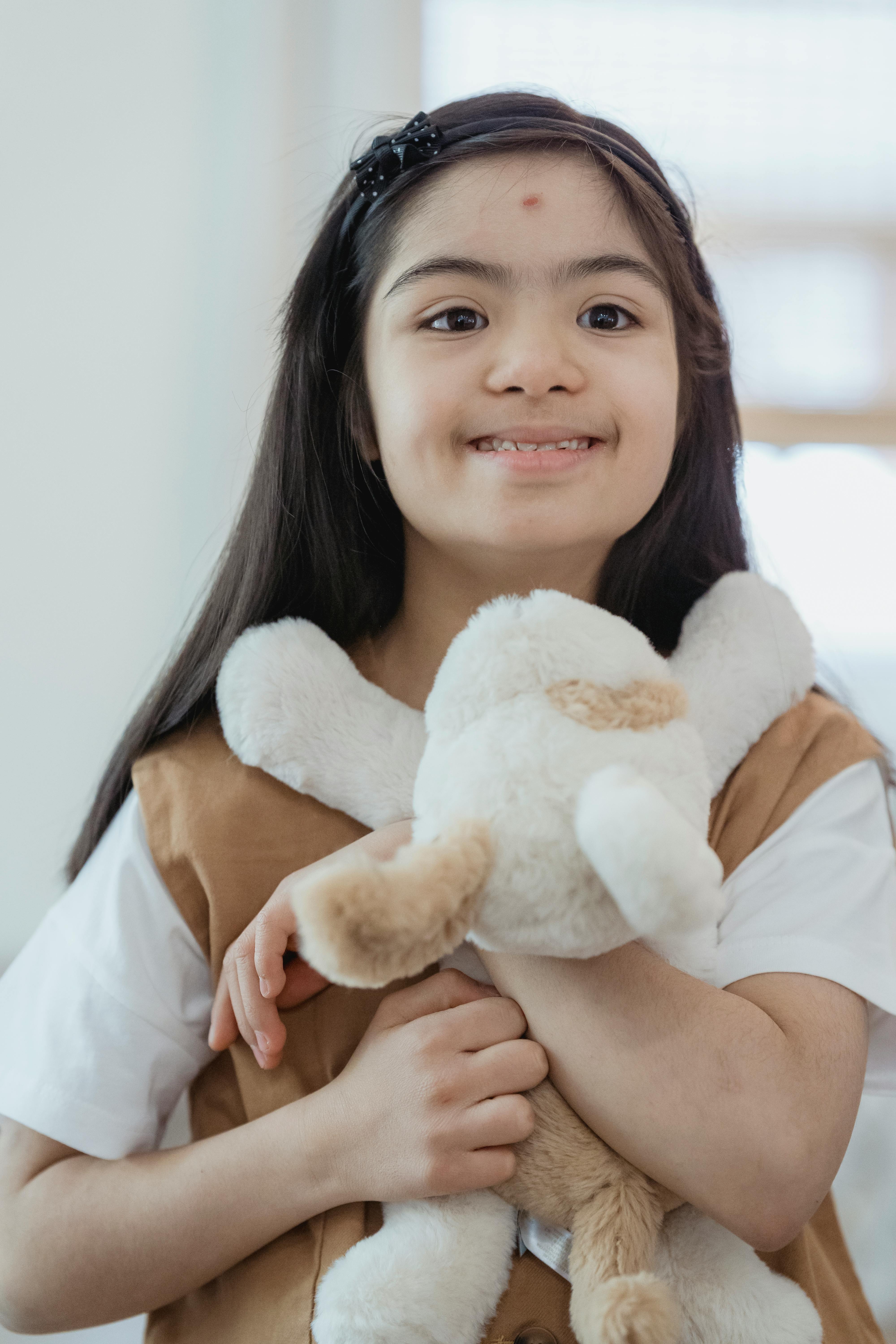 A Young Girl Smiling while Hugging Her Stuffed Toy · Free Stock Photo