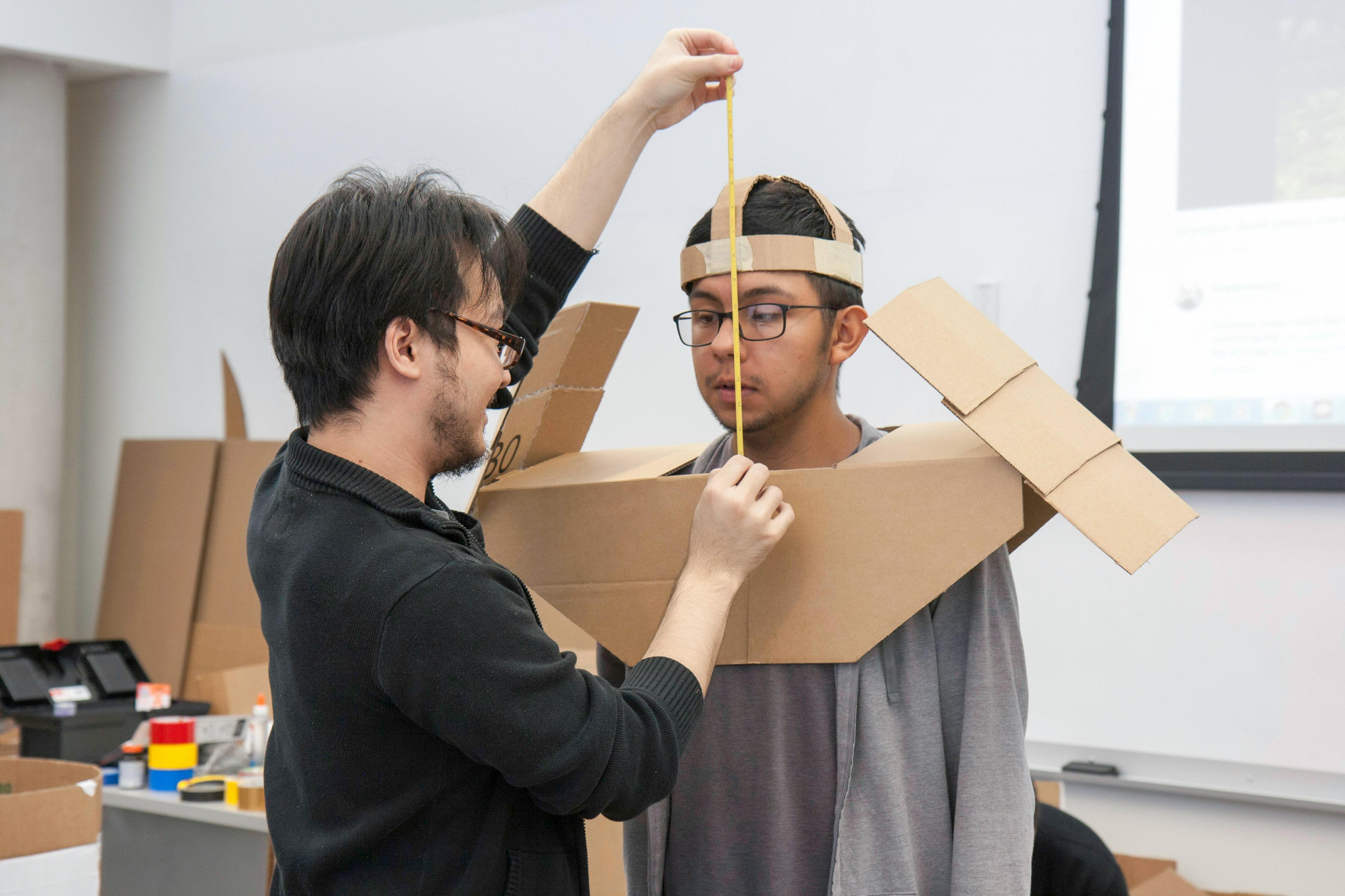 Man measuring his Colleague while wearing Cut-out Carton Boxes · Free ...