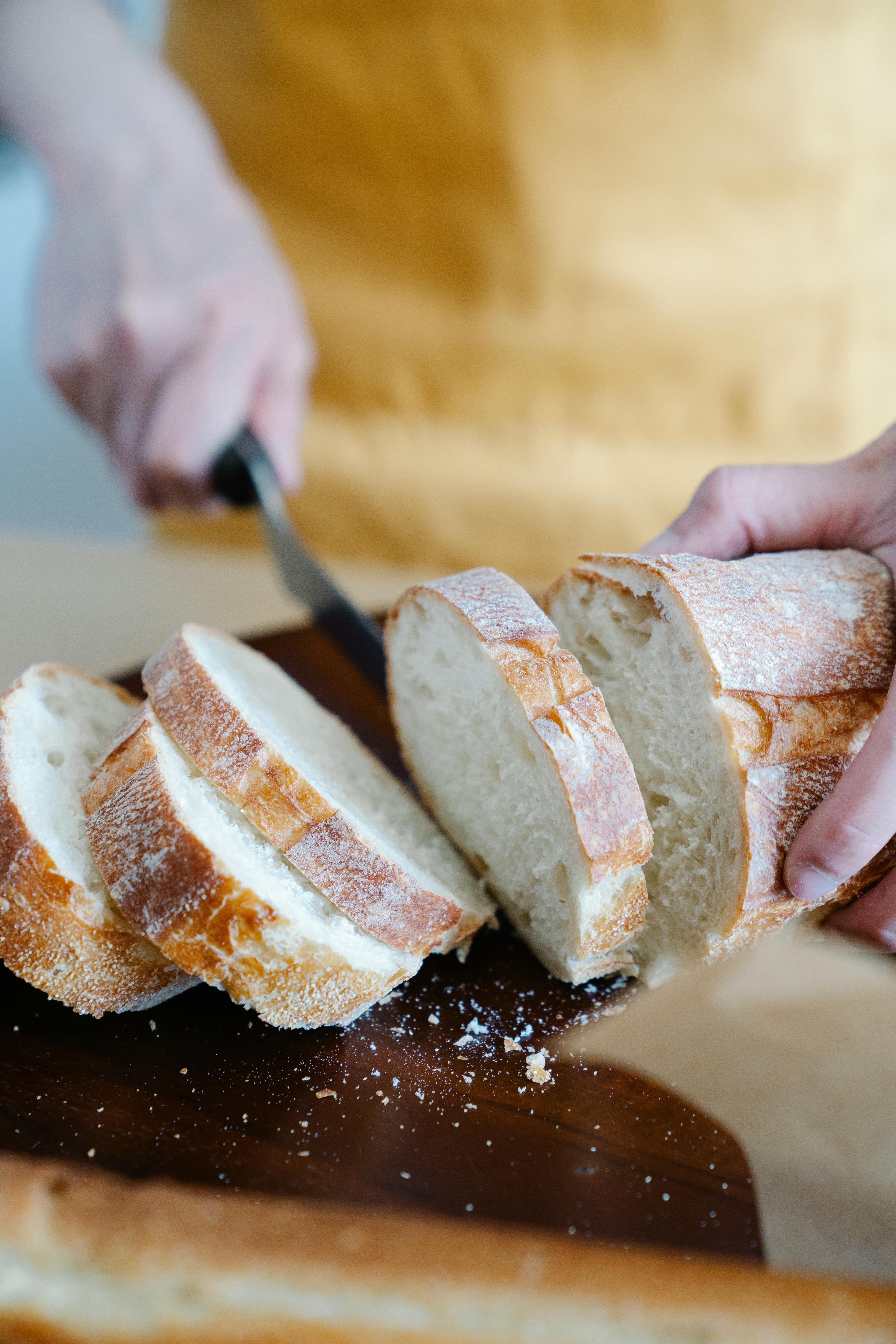 Person Slicing Bread on Brown Wooden Board · Free Stock Photo
