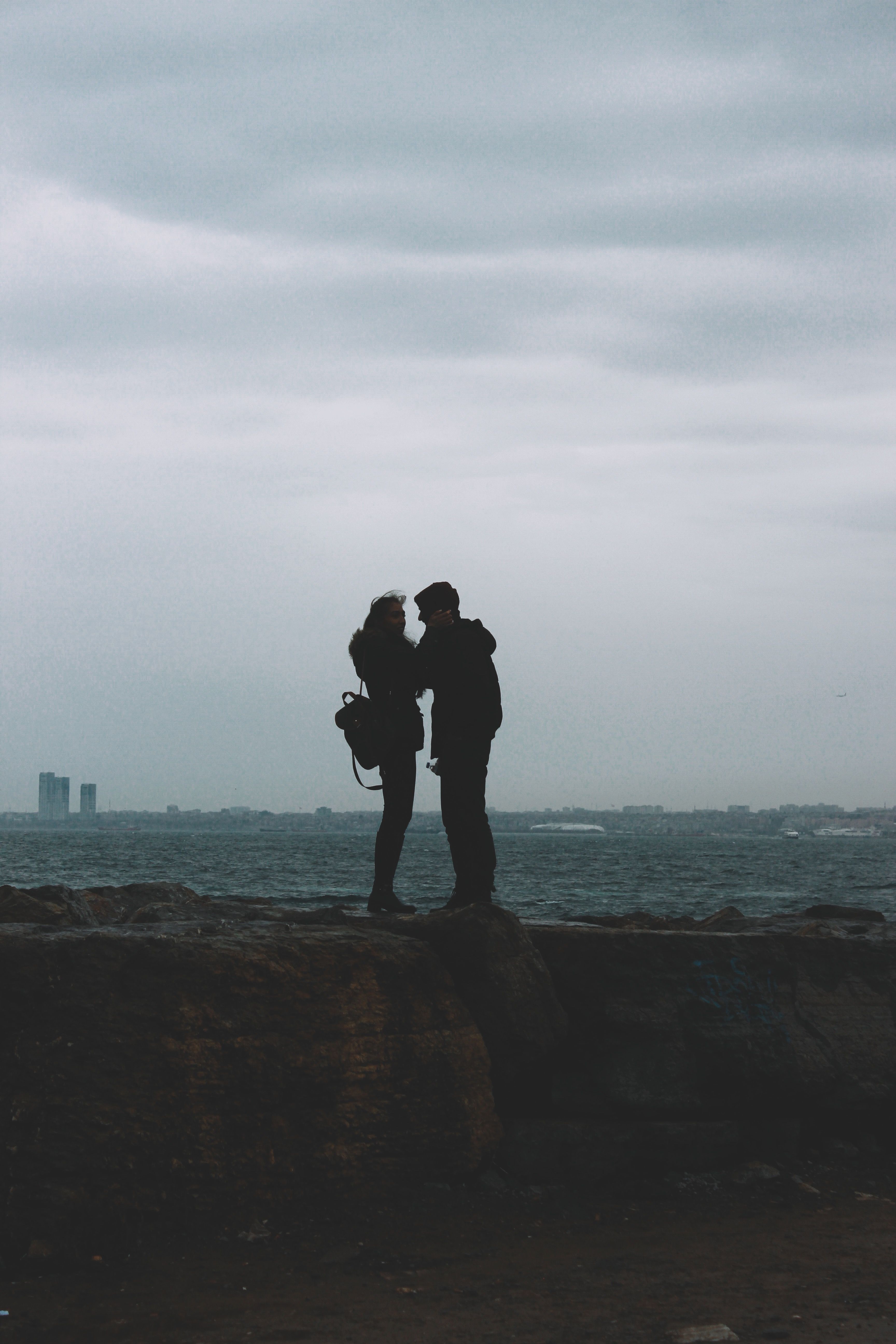 Silhouette of couple standing on cliff washed by sea · Free Stock Photo