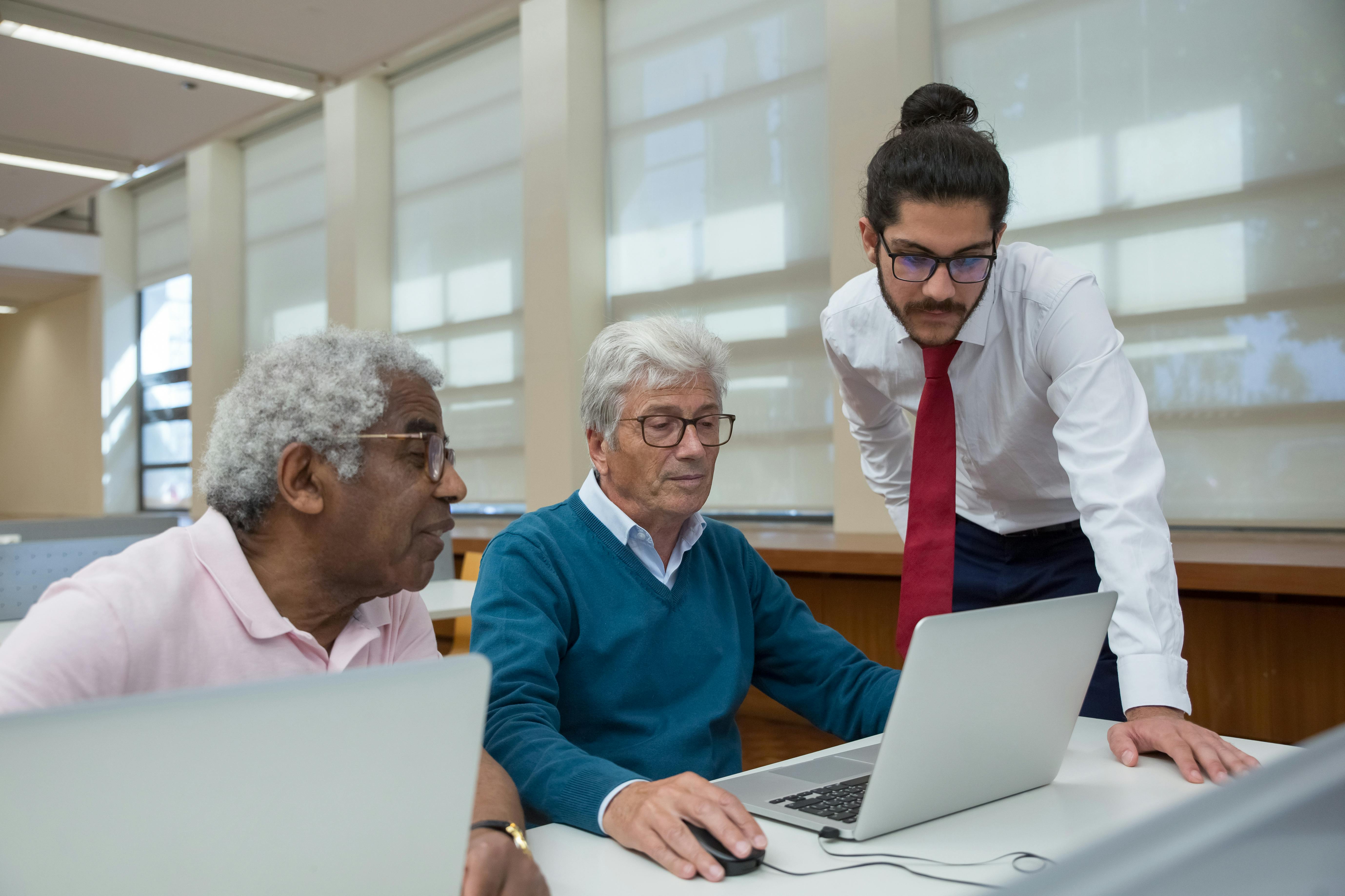 A Man Standing Beside the Elderly Using a Laptop · Free Stock Photo