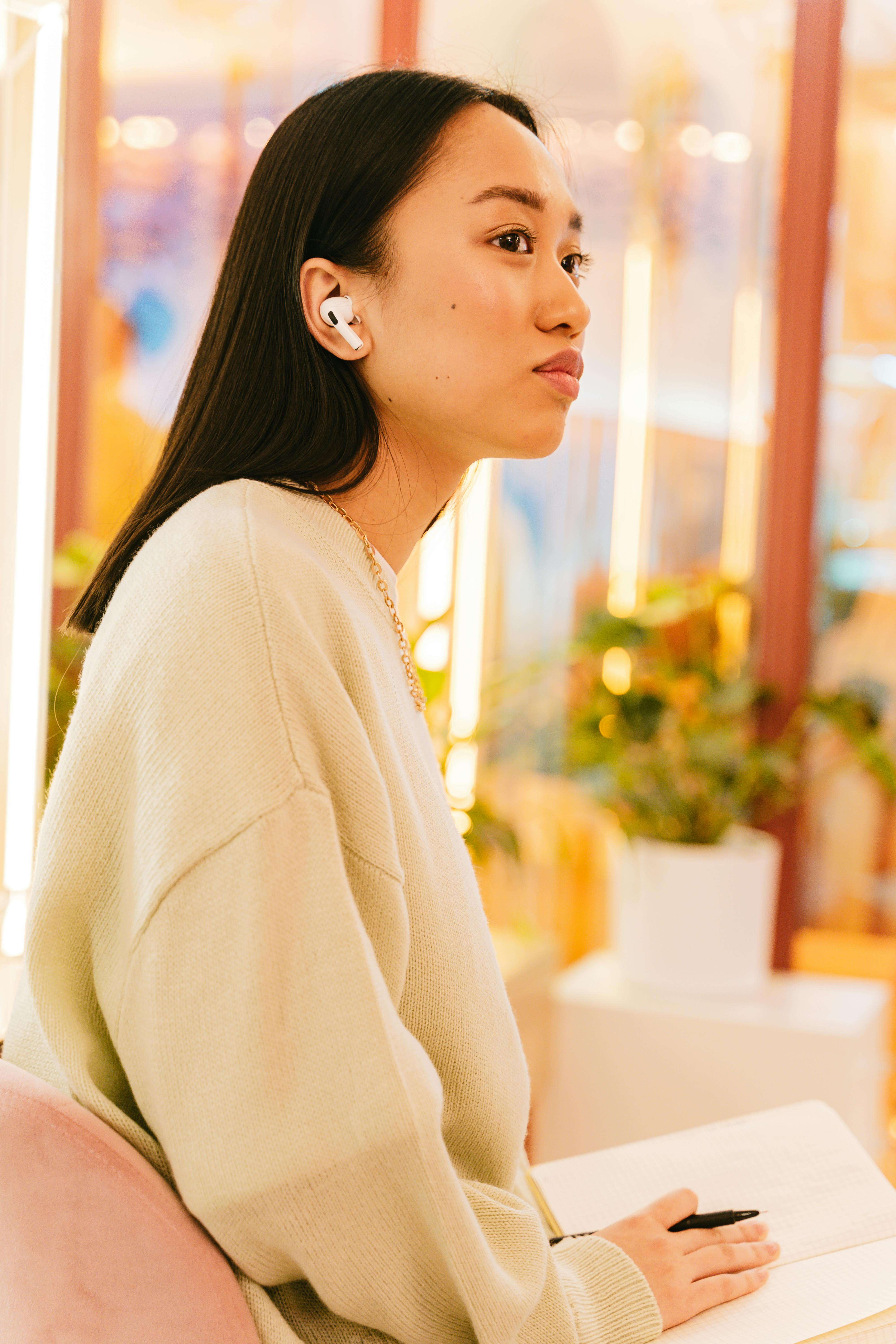 Woman in Beige Sweater Wearing Earphone Taking Notes · Free Stock Photo