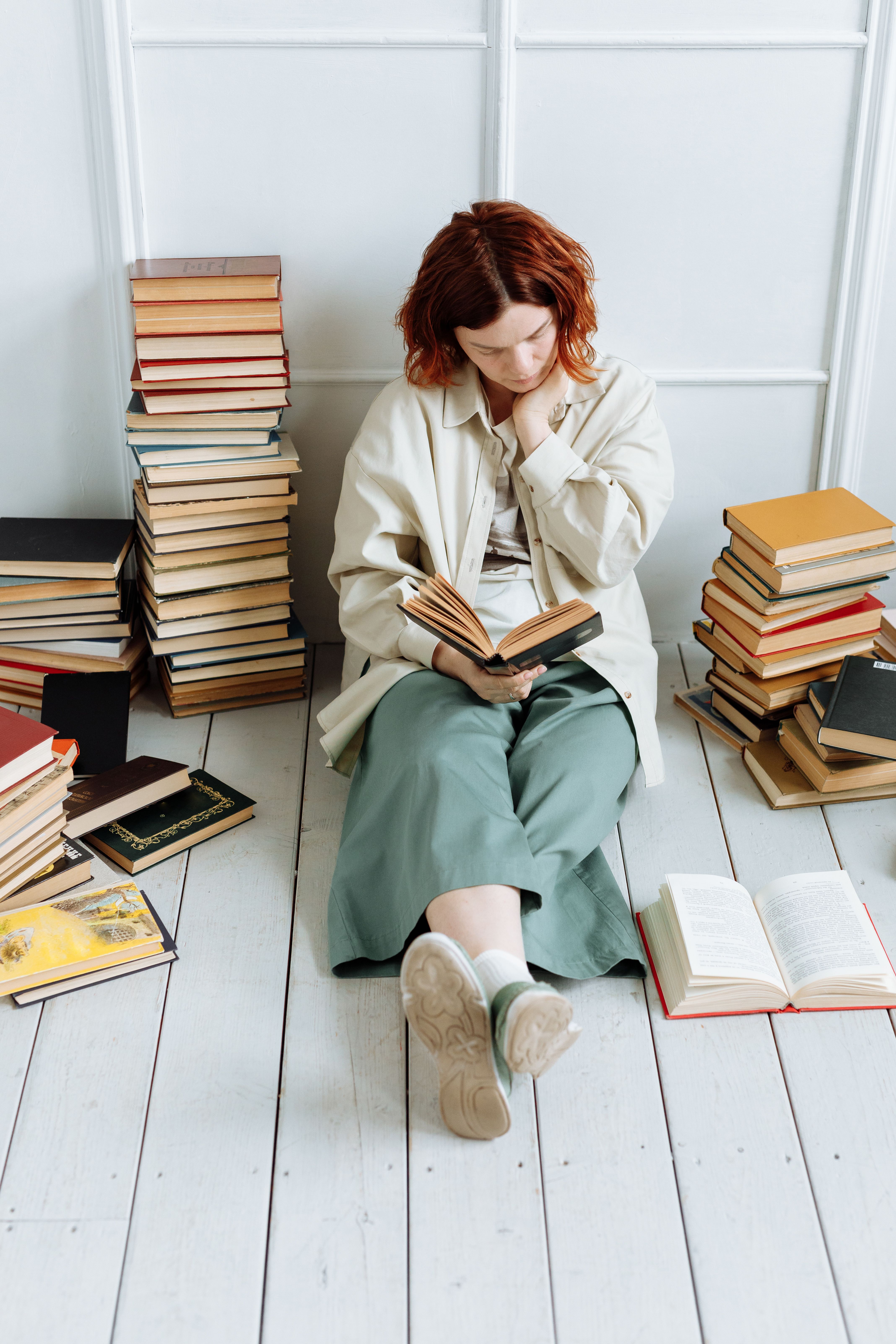 Woman in White Long Sleeves Reading a Book while Sitting on a Wooden ...