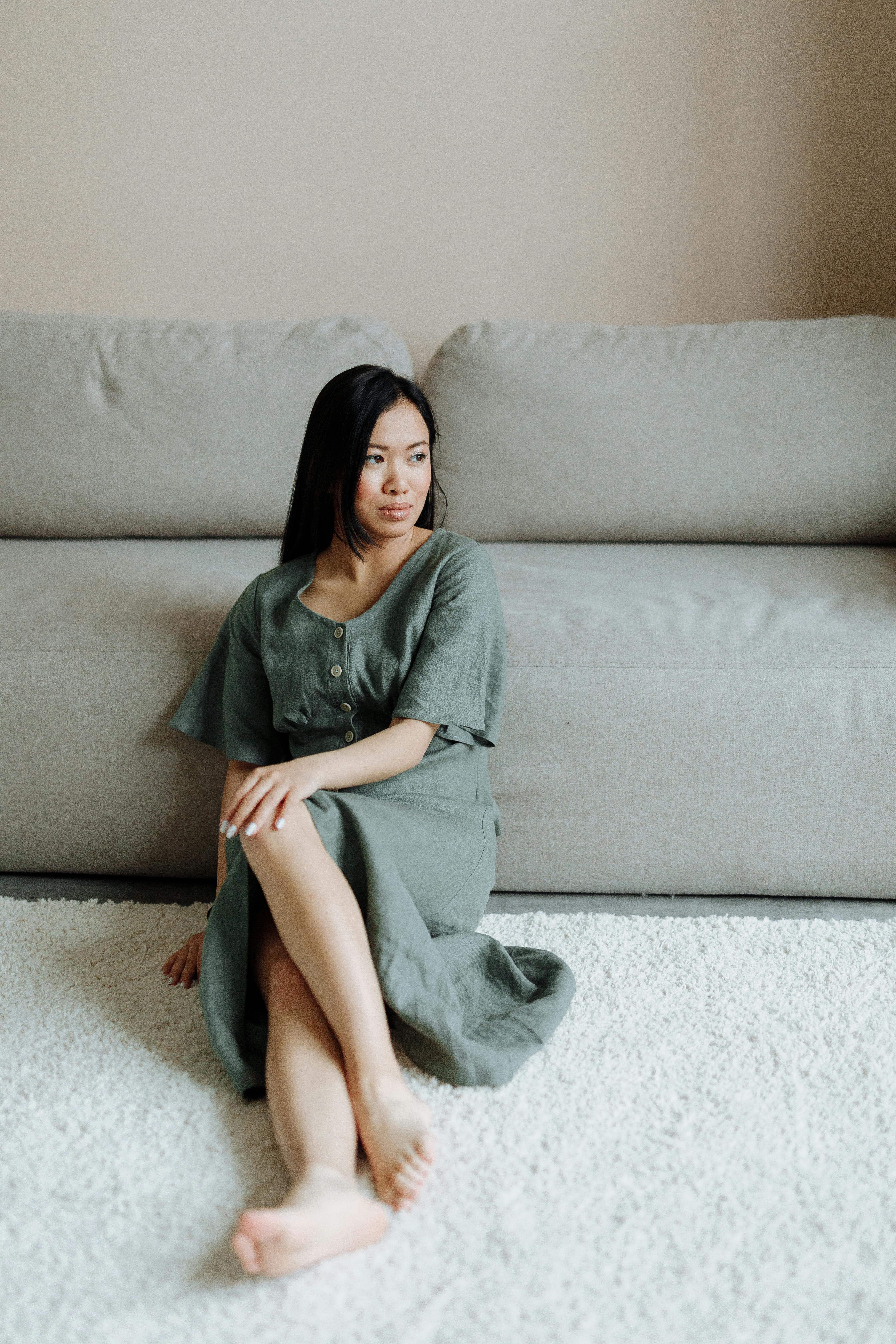 Woman Sitting on White Rug while Leaning on Grey Sofa · Free Stock Photo