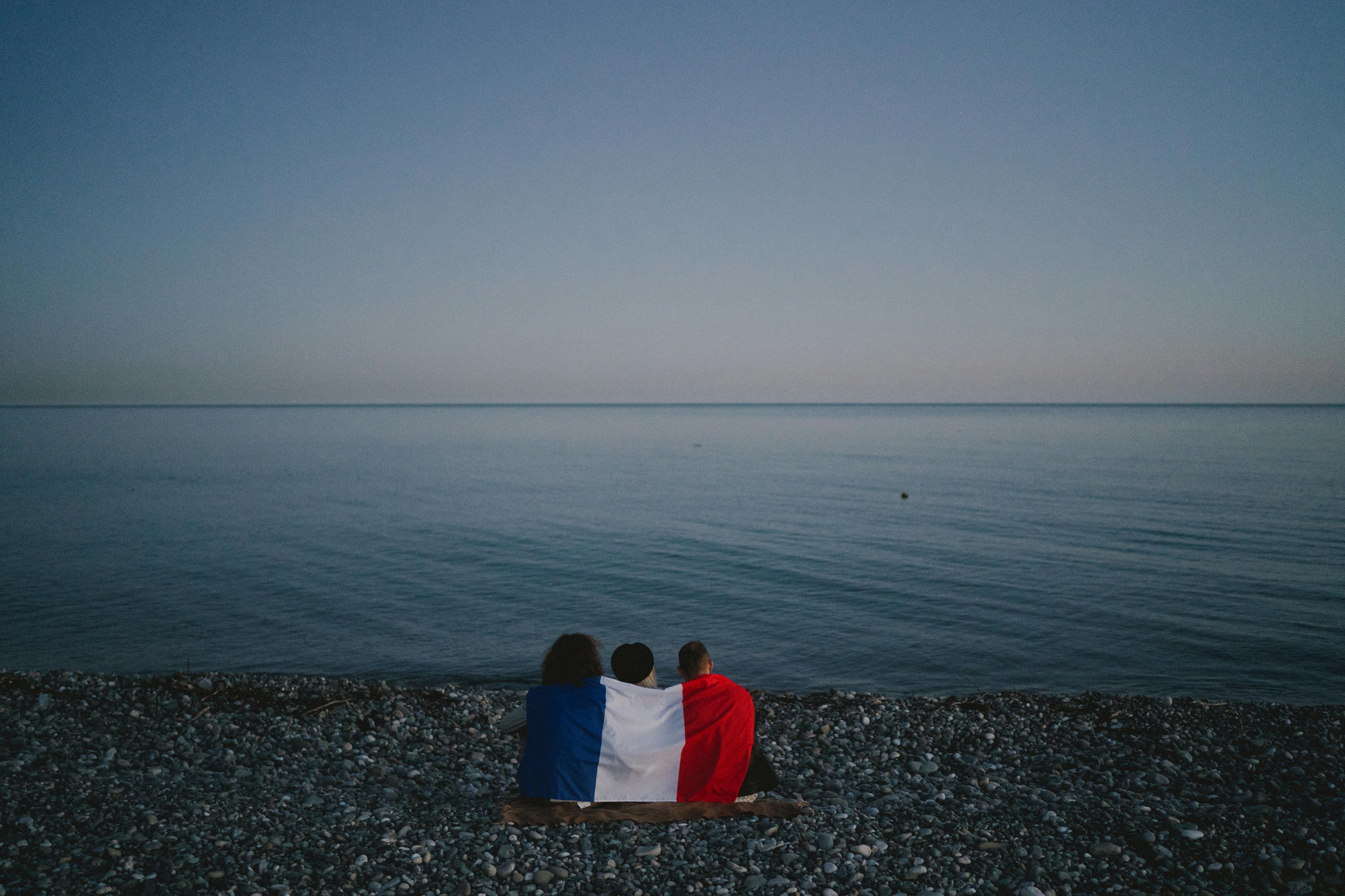 Friends Sitting on a Rocky Shore with the Flag of France on Their Back ...