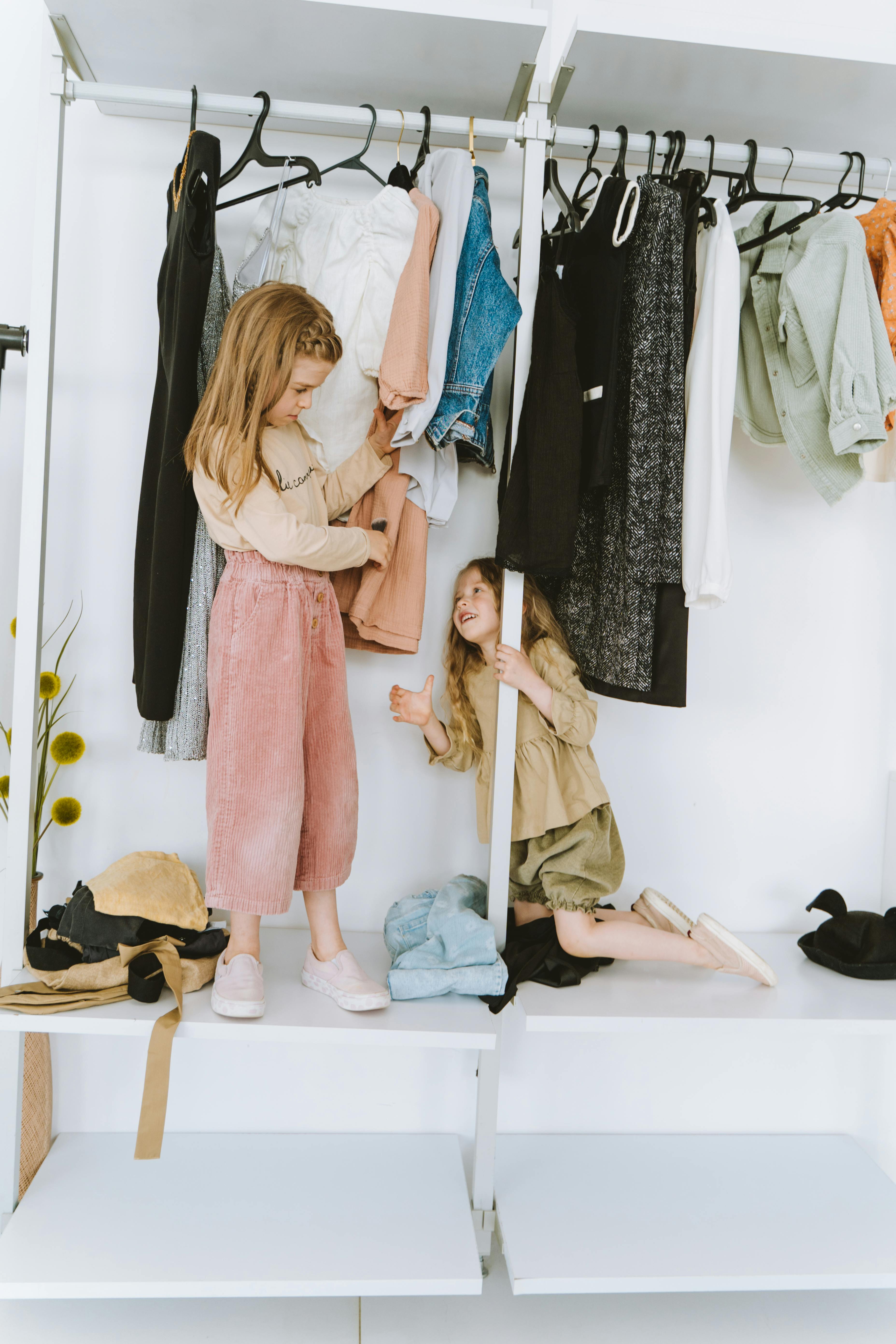 Girls Playing on the Cabinet with Hanging Clothes · Free Stock Photo