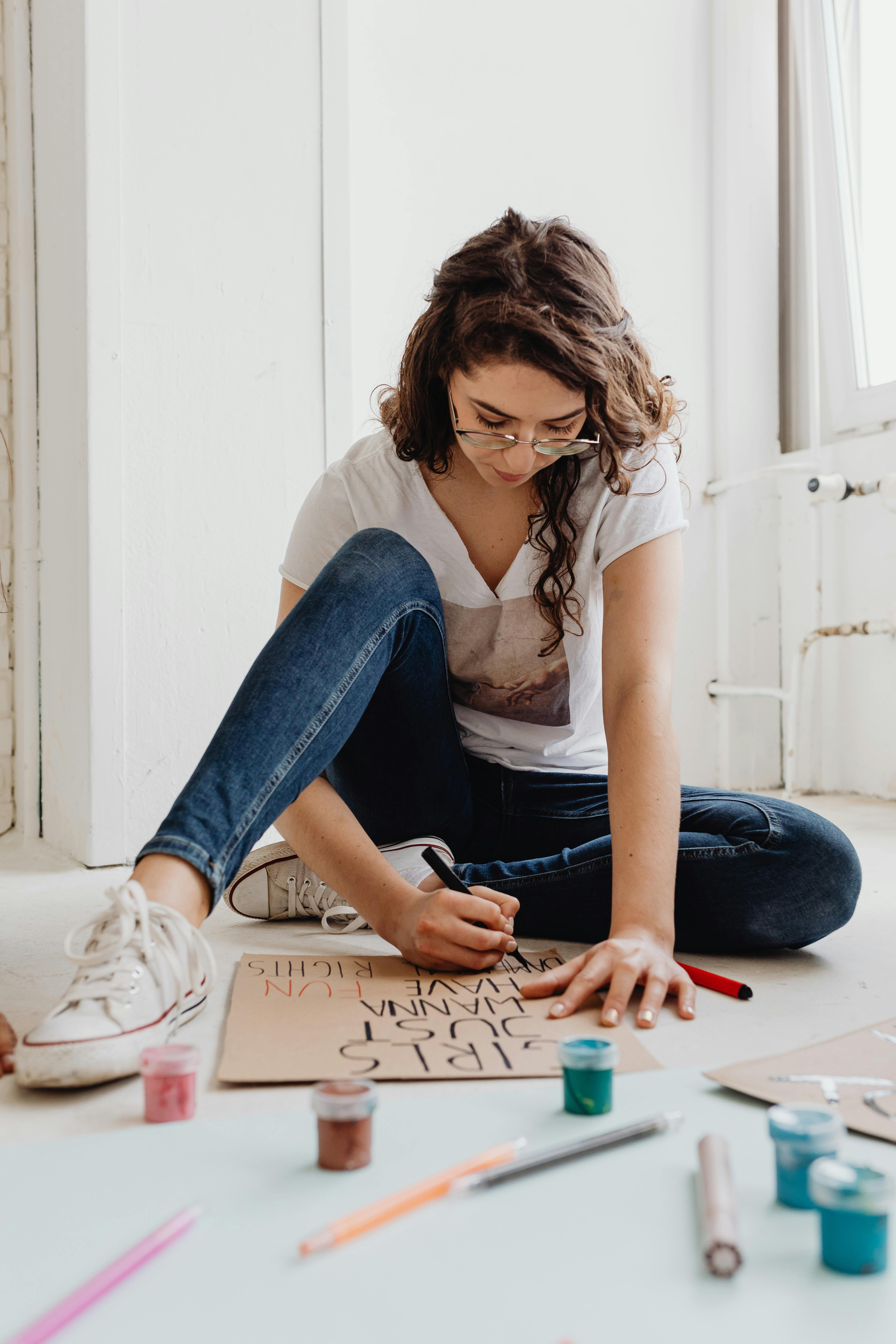 Woman Sitting on the Floor While Writing on a Cardboard · Free Stock Photo