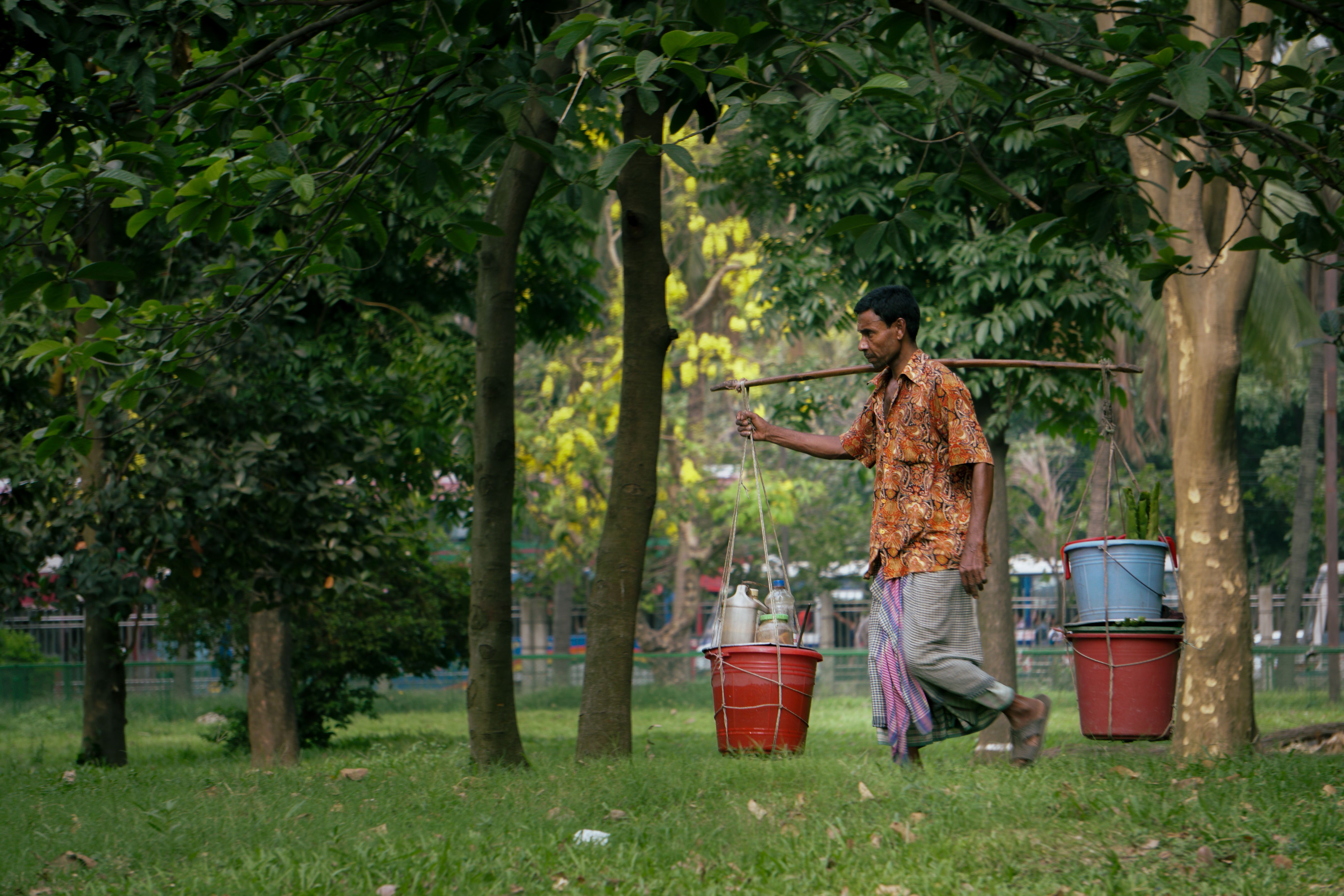 Man Carrying Buckets on Wooden Staff through Park · Free Stock Photo