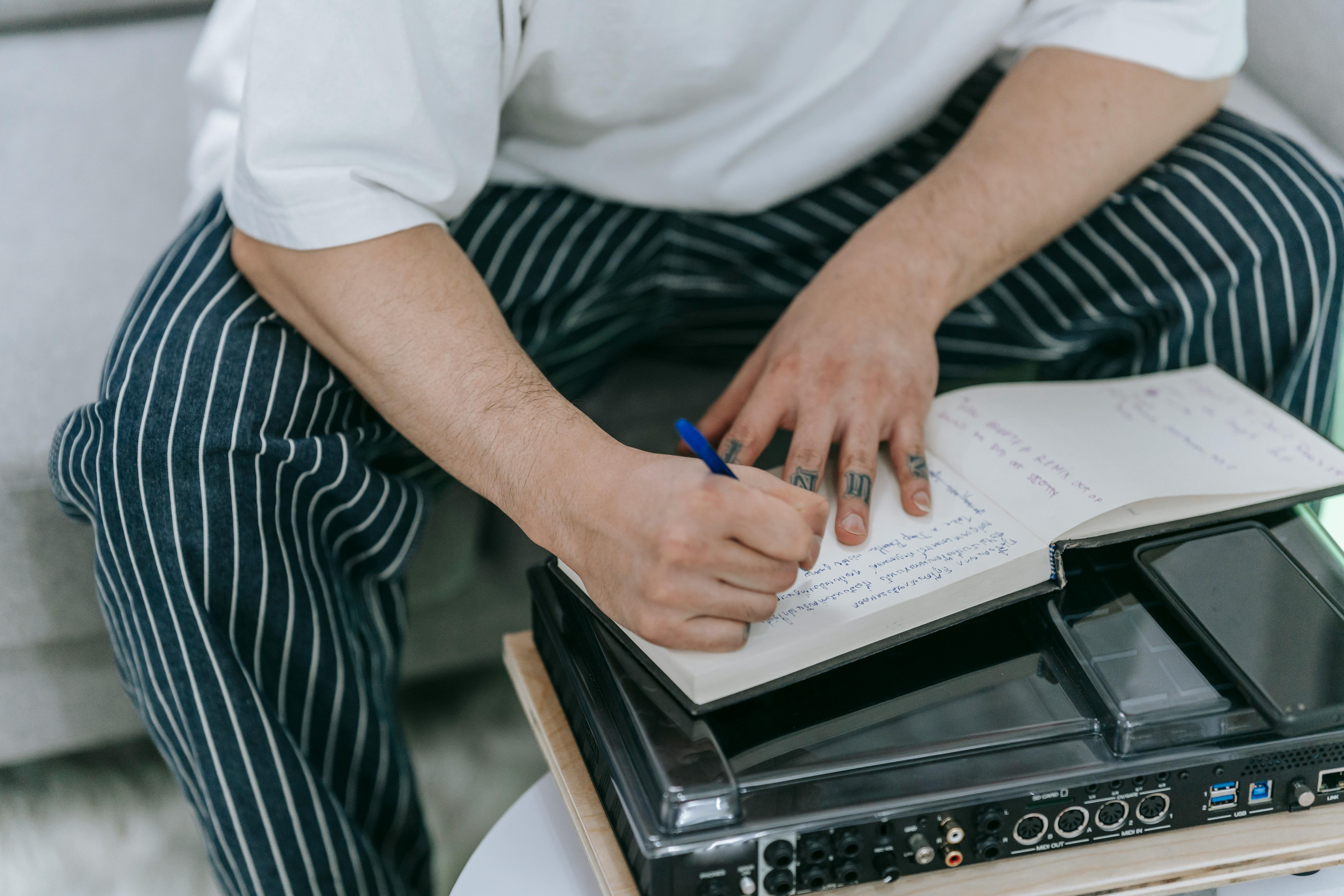 Man in Black and White Strip Pants Writing Notebook · Free Stock Photo