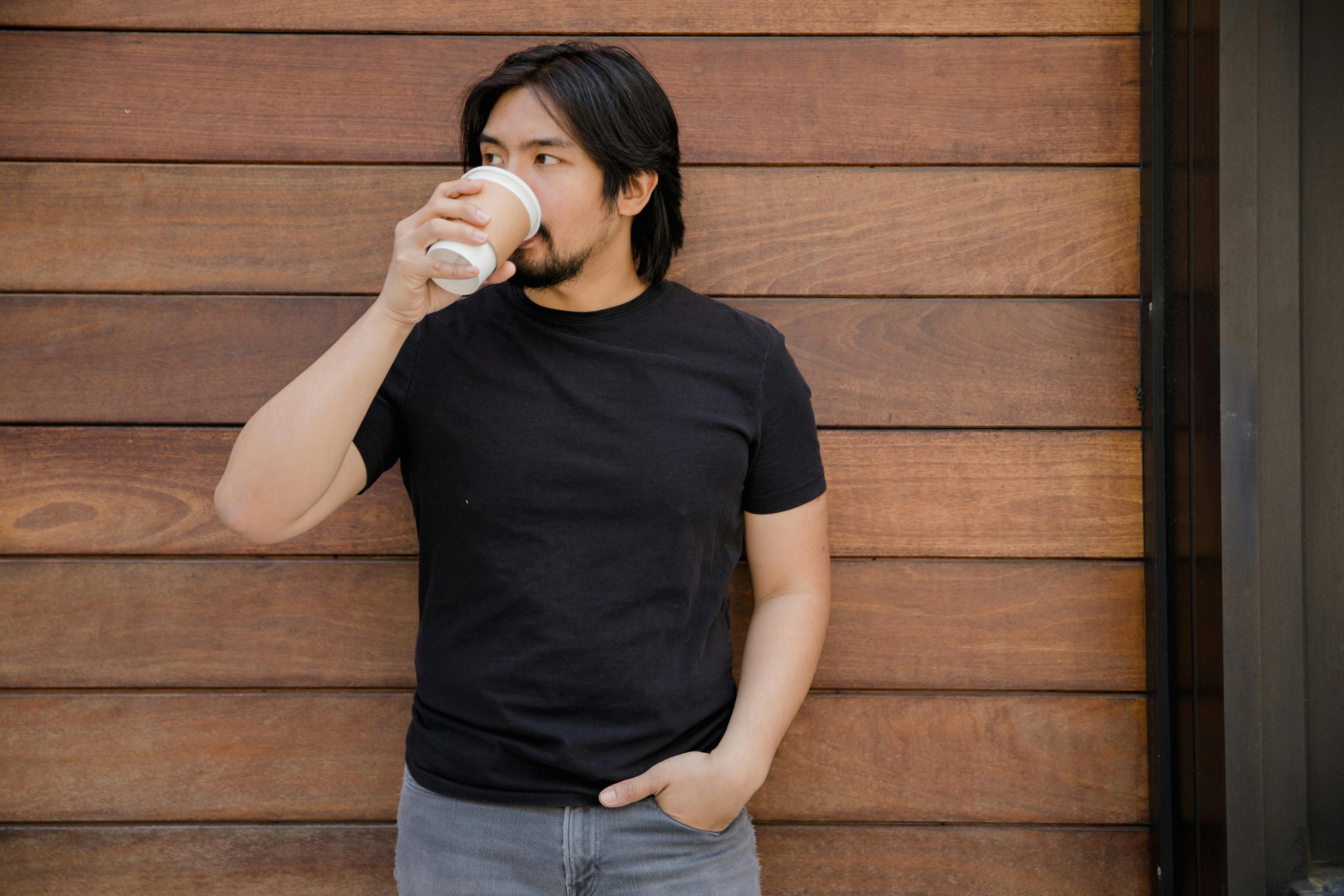 Man Standing Near the Wooden Wall Drinking Coffee · Free Stock Photo