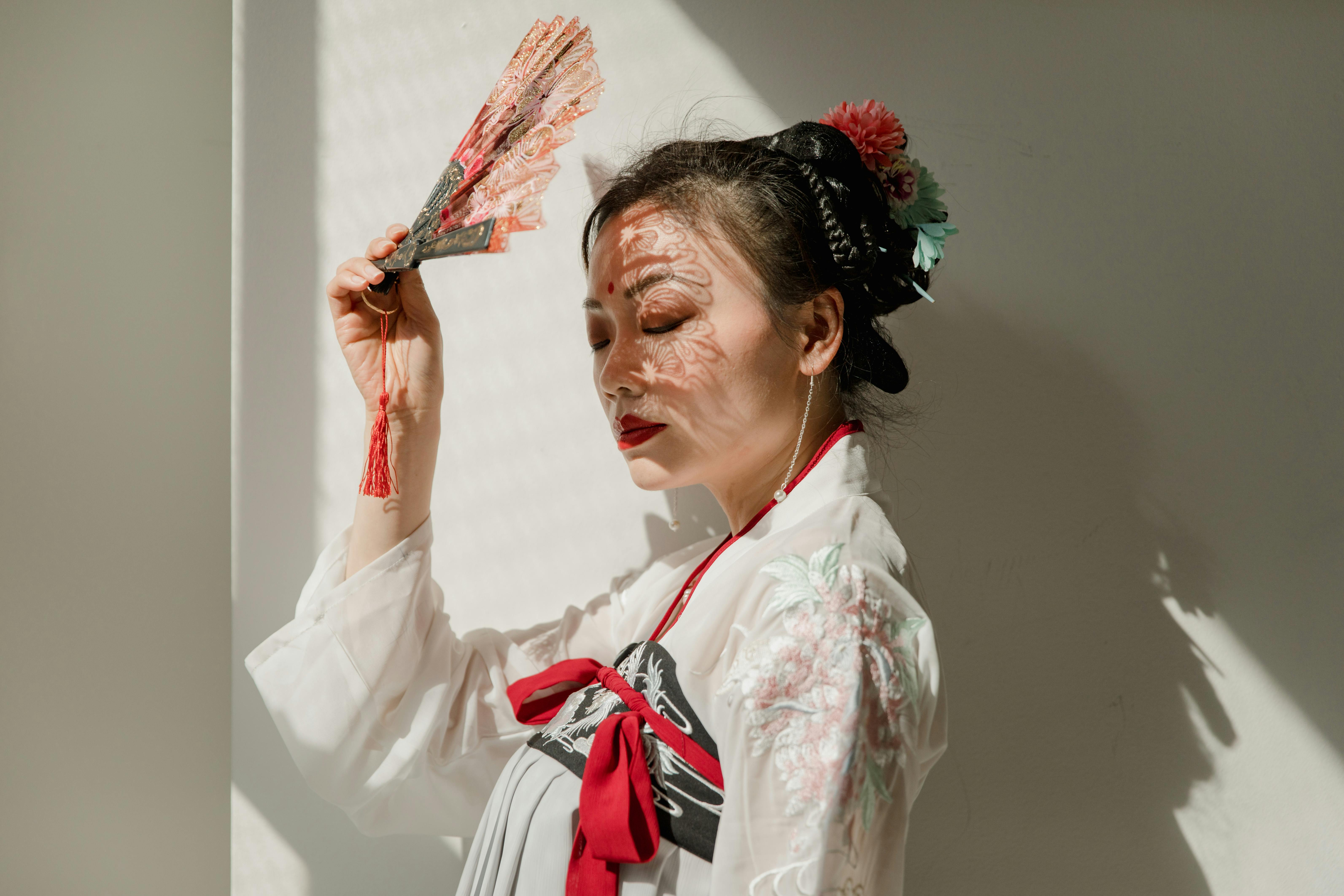 A Woman Holding a Hand Fan while Eyes Closed · Free Stock Photo