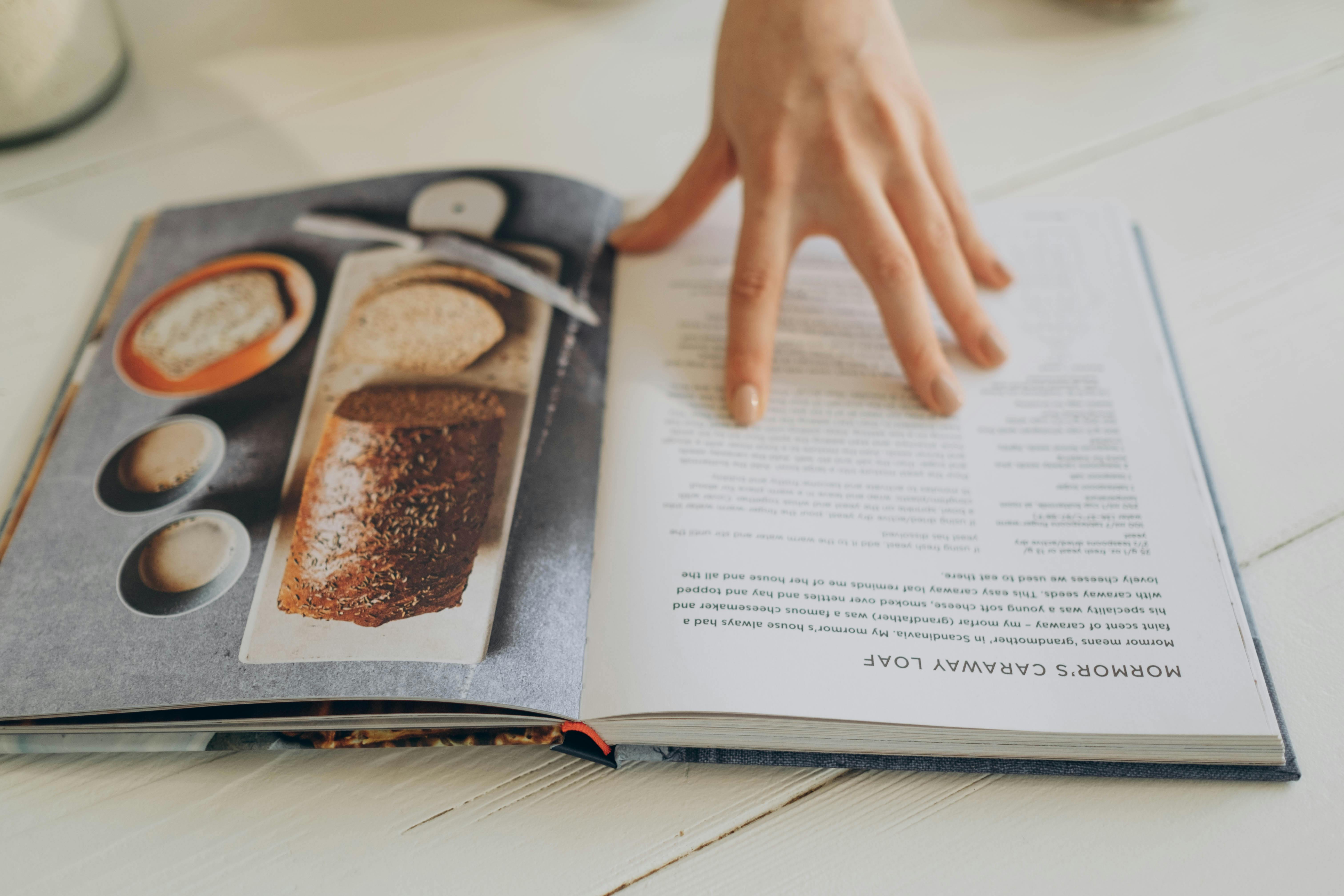 A Hand on an Open Cookbook · Free Stock Photo