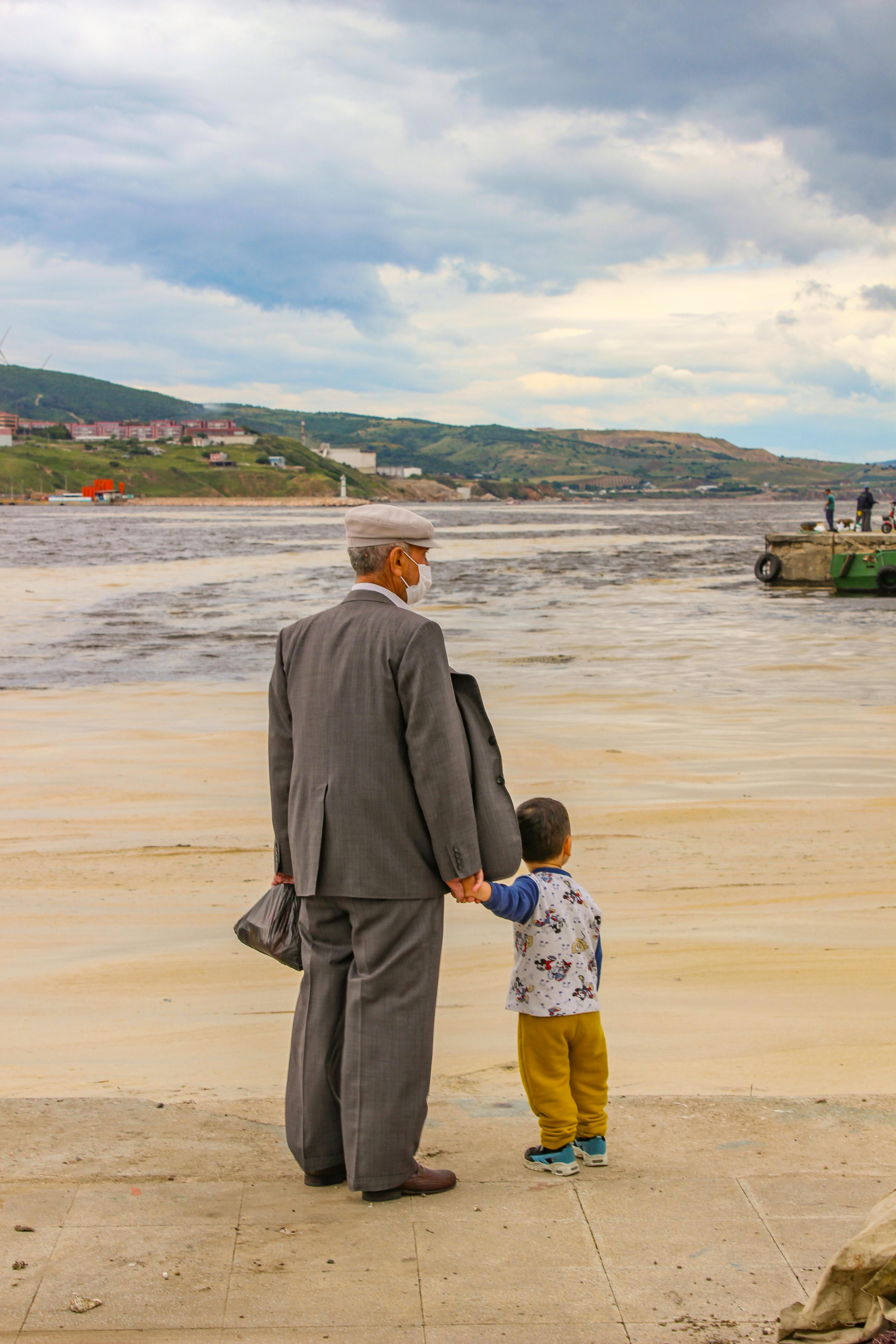 An Elderly Man Holding and a Child Standing on Pavement · Free Stock Photo