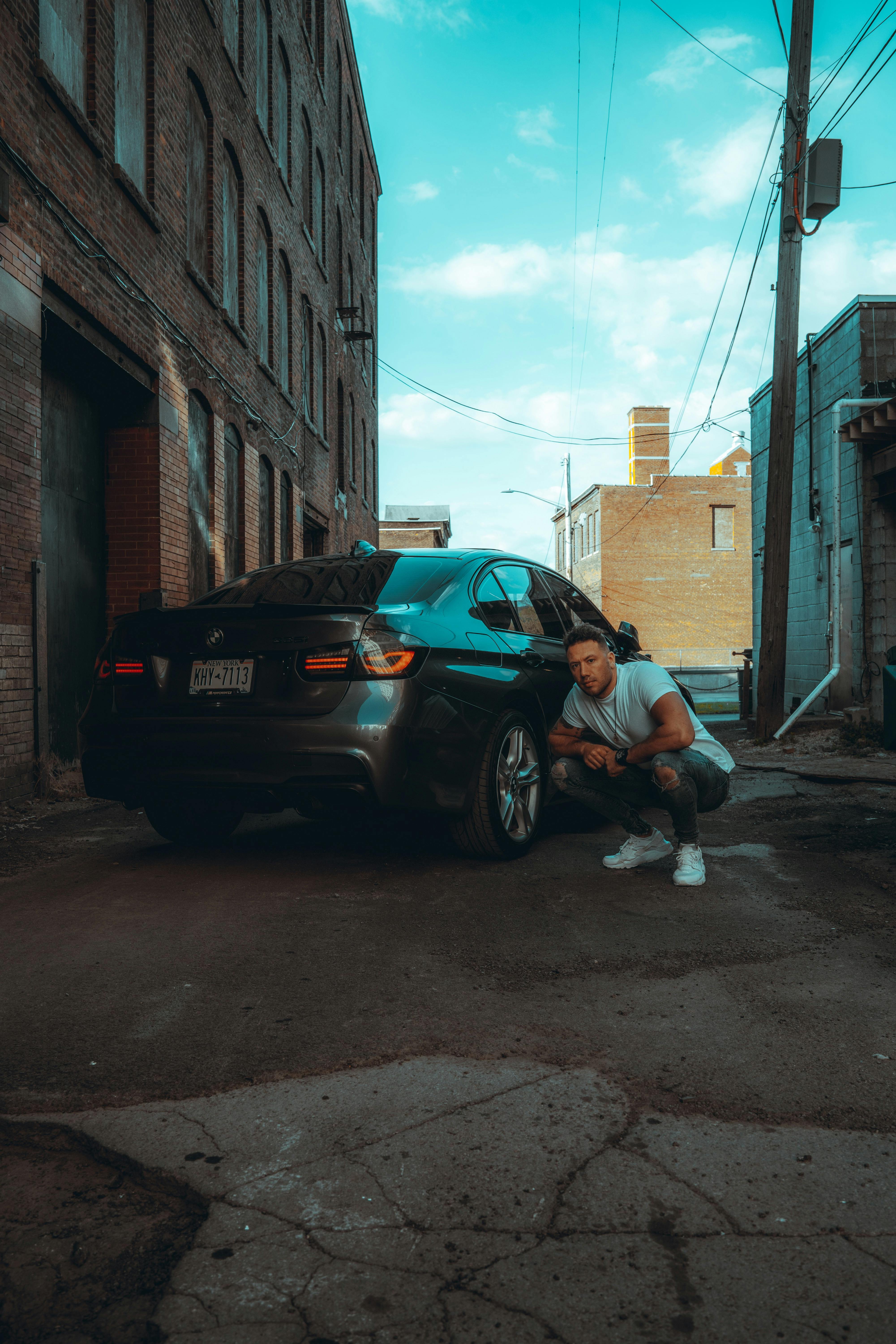 Man Crouching near Car on City Street · Free Stock Photo
