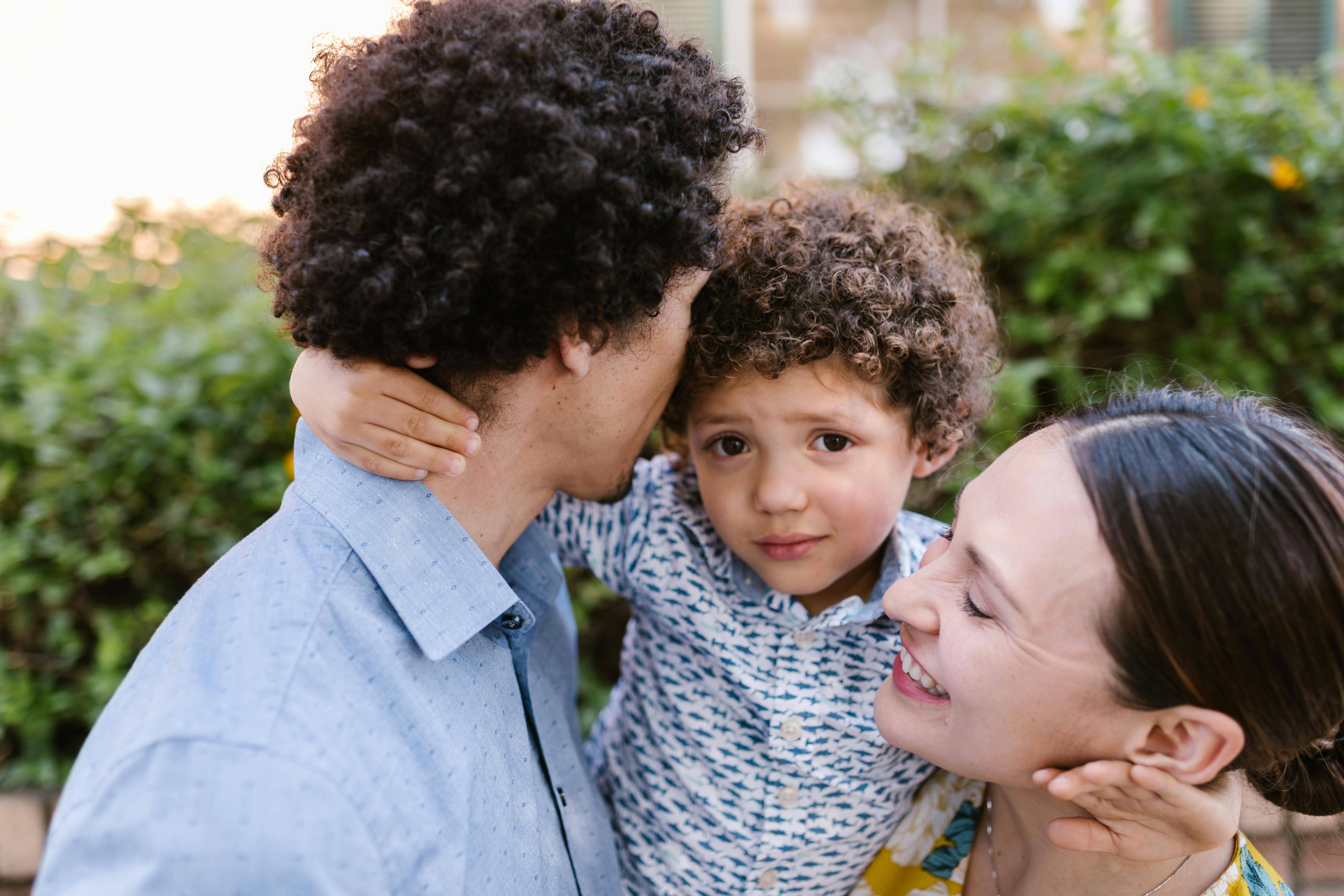 Little Boy with Curly Hair in His Parents Arms · Free Stock Photo
