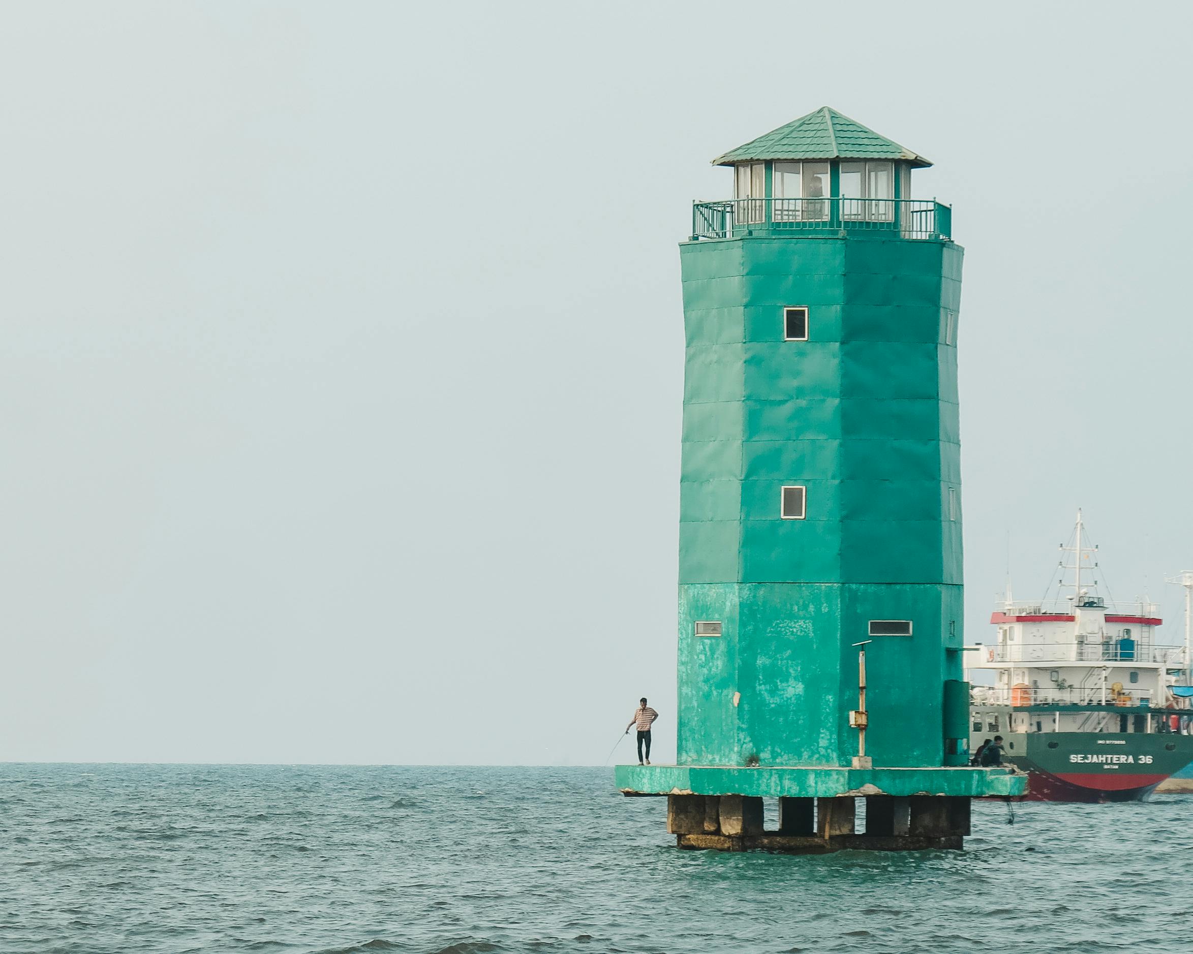 Man Walking on Platform under Lighthouse at Sea · Free Stock Photo