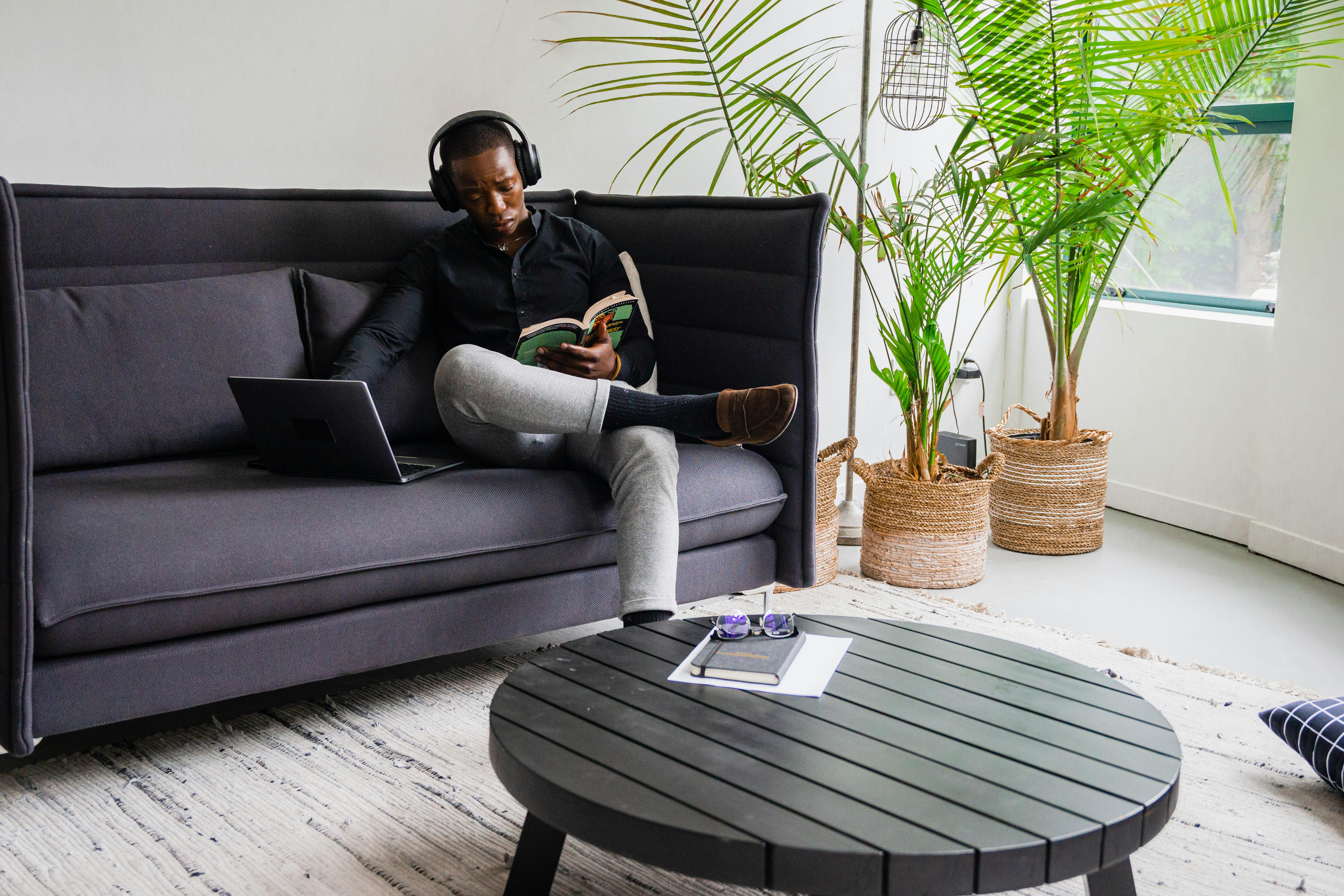 A Man Reading a Book while Sitting on a Couch · Free Stock Photo