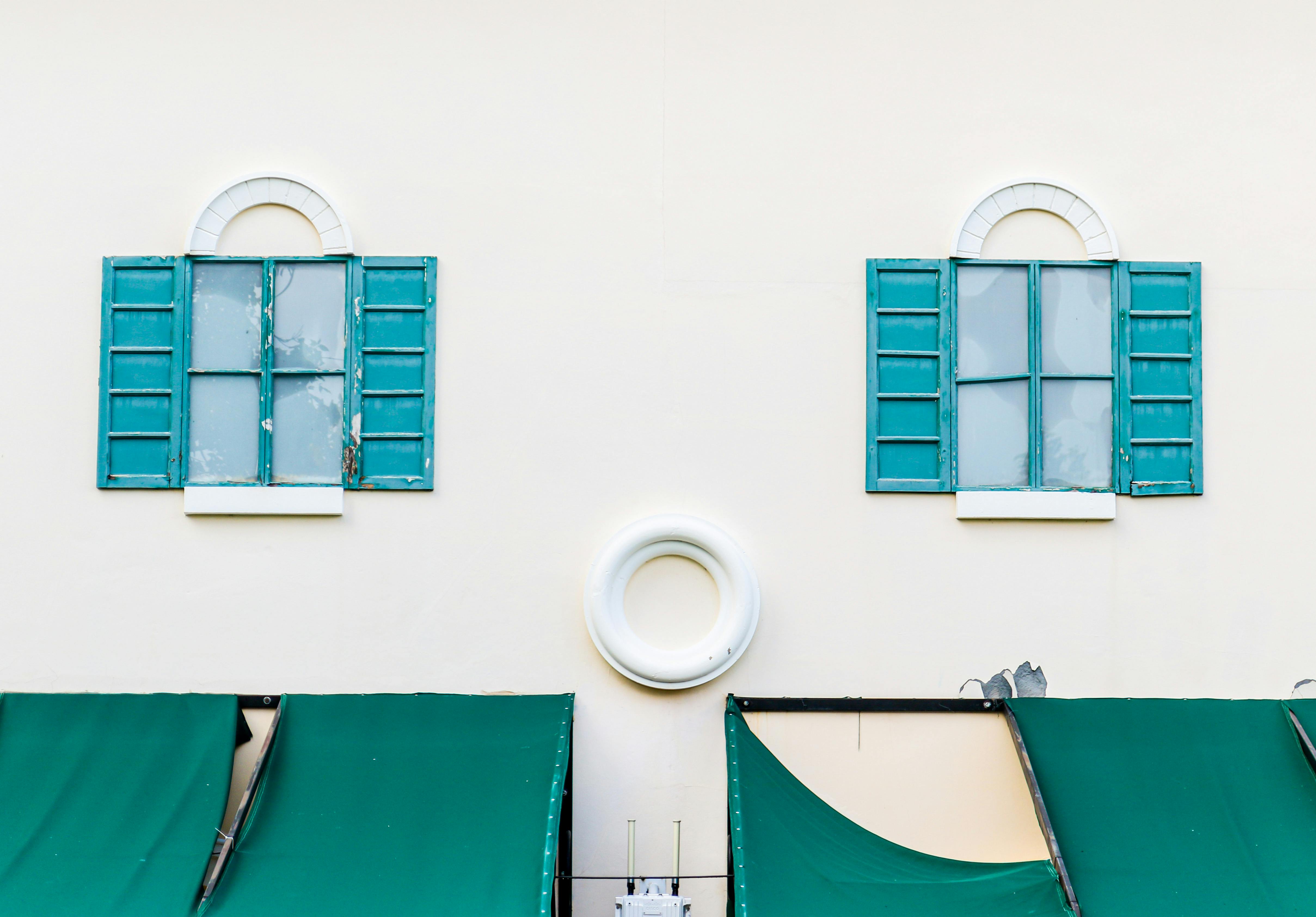A White Concrete Building with Blue Window Shutters and Green Canopies ...