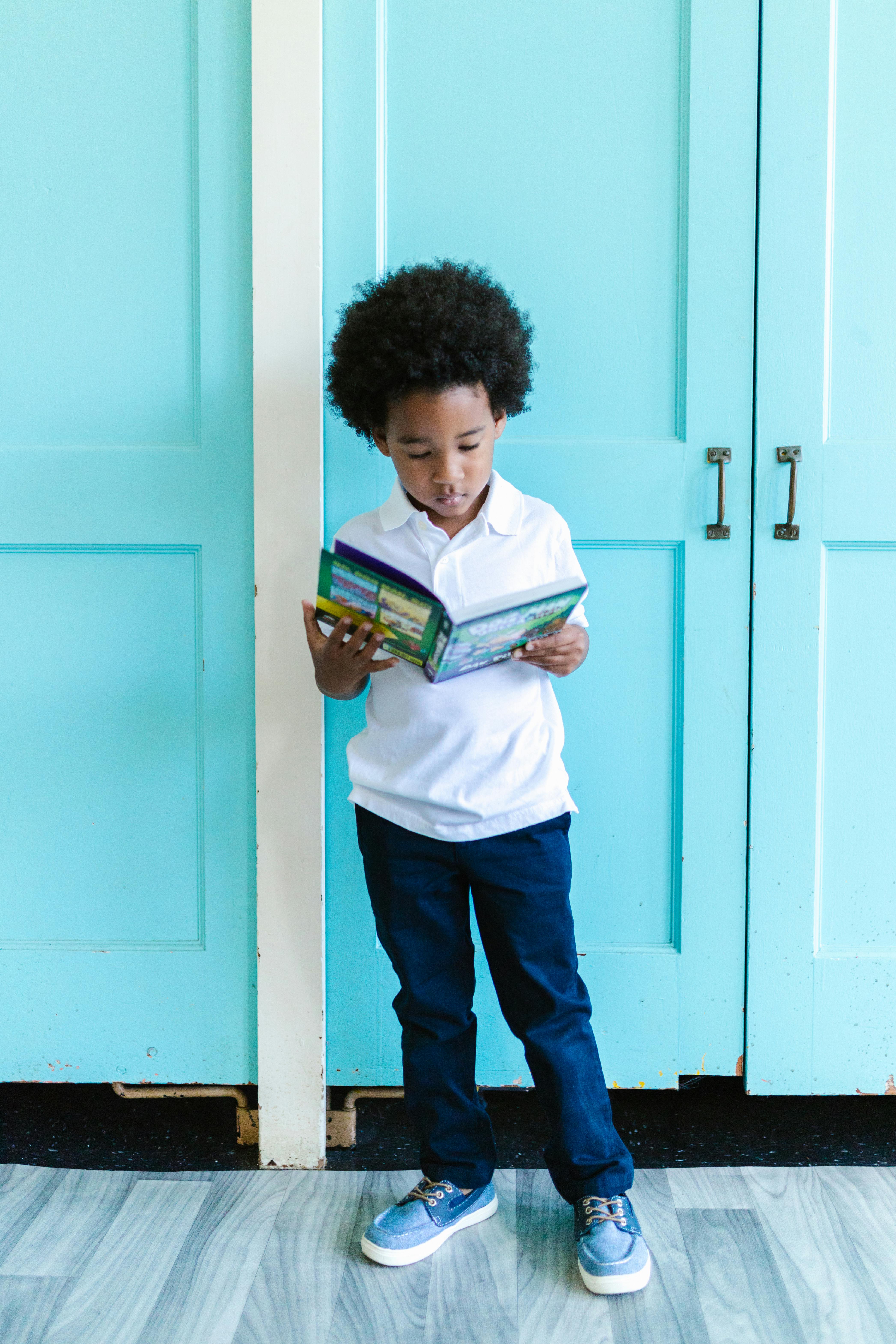 A Cute Boy Standing While Reading a Book · Free Stock Photo