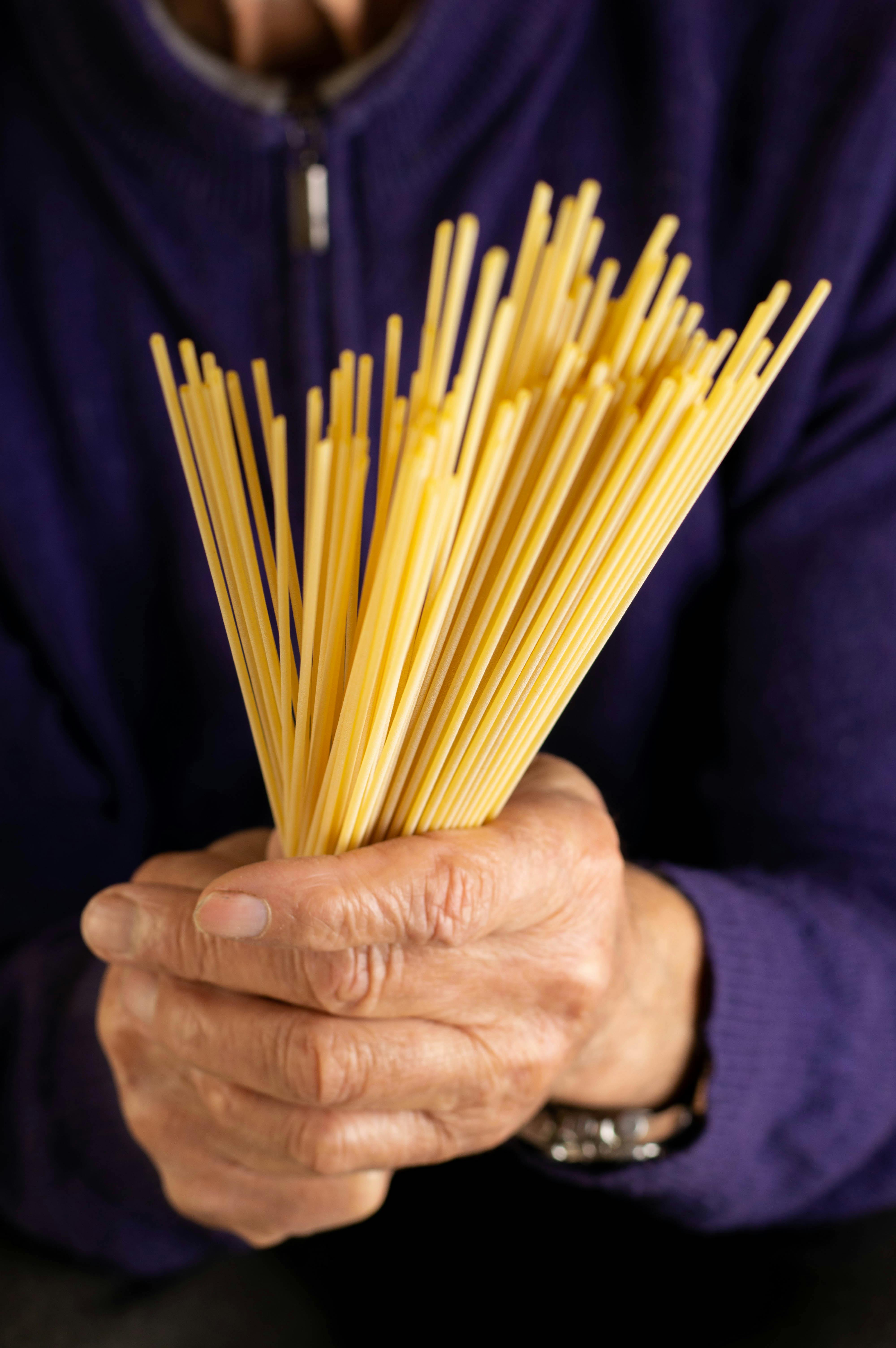 Close-up of a Man Holding Raw Spaghetti Pasta · Free Stock Photo