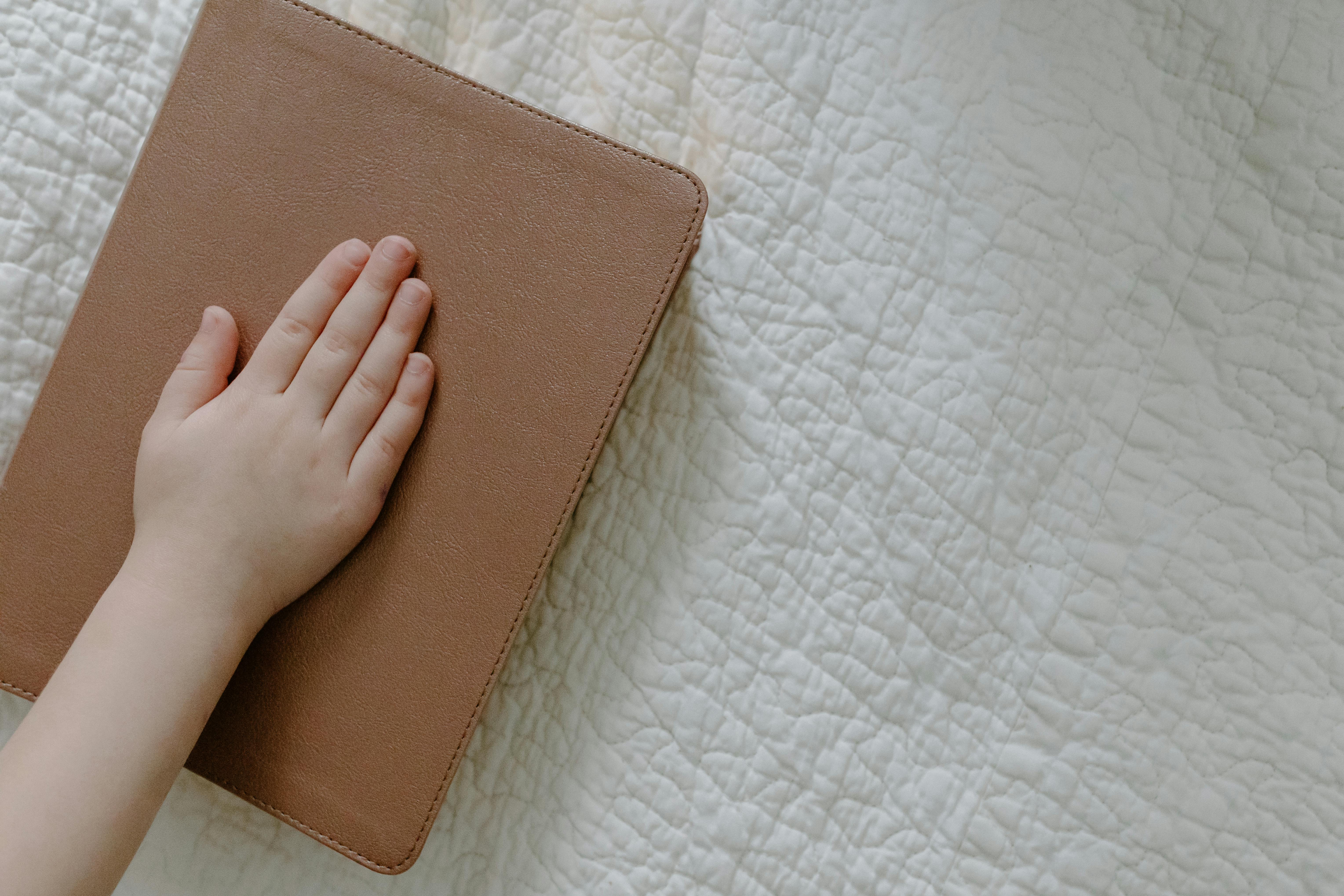 Hand of a Person on a Brown Book · Free Stock Photo