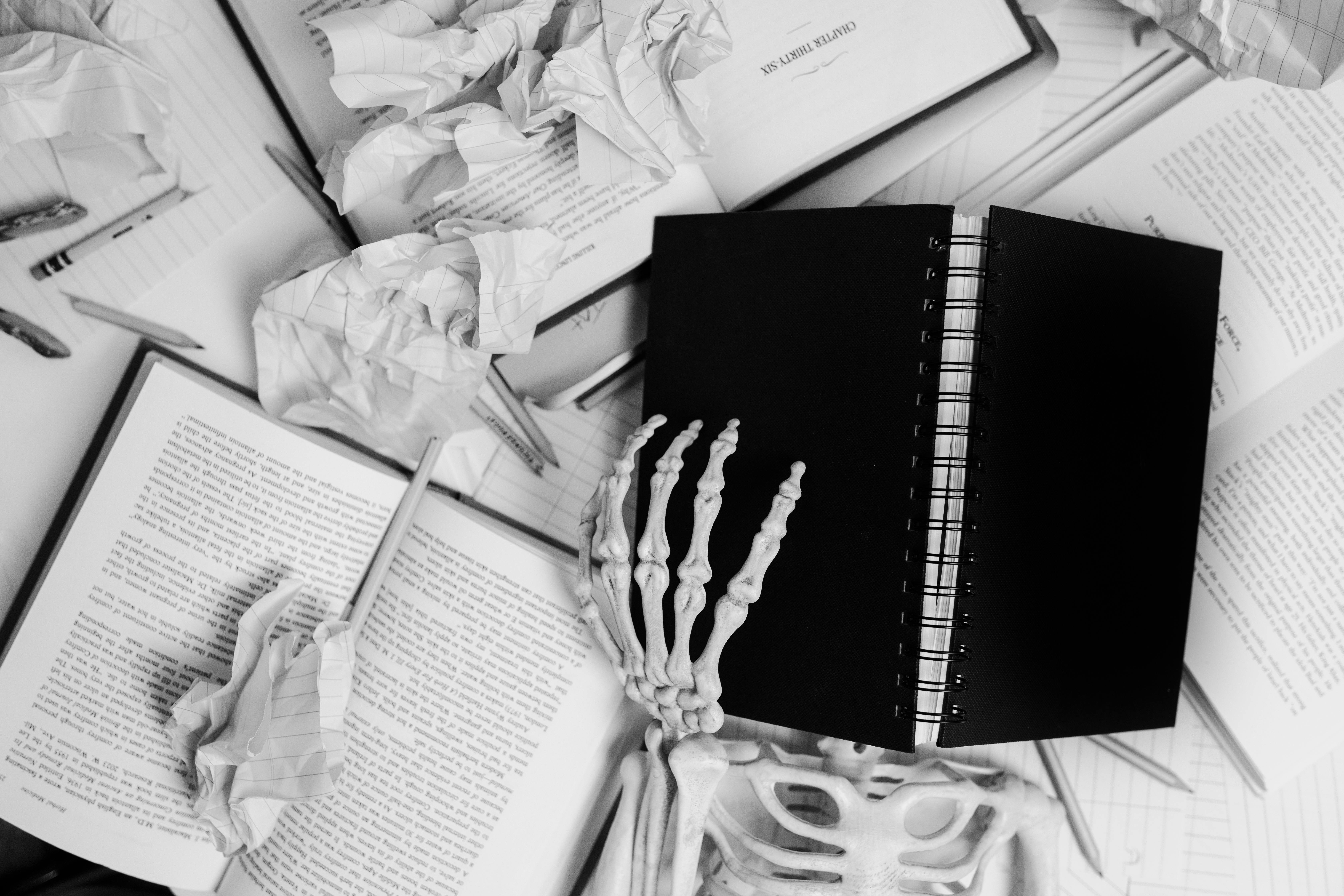 A Skeleton Hand on a Black Spiral Note Book Beside Books · Free Stock Photo