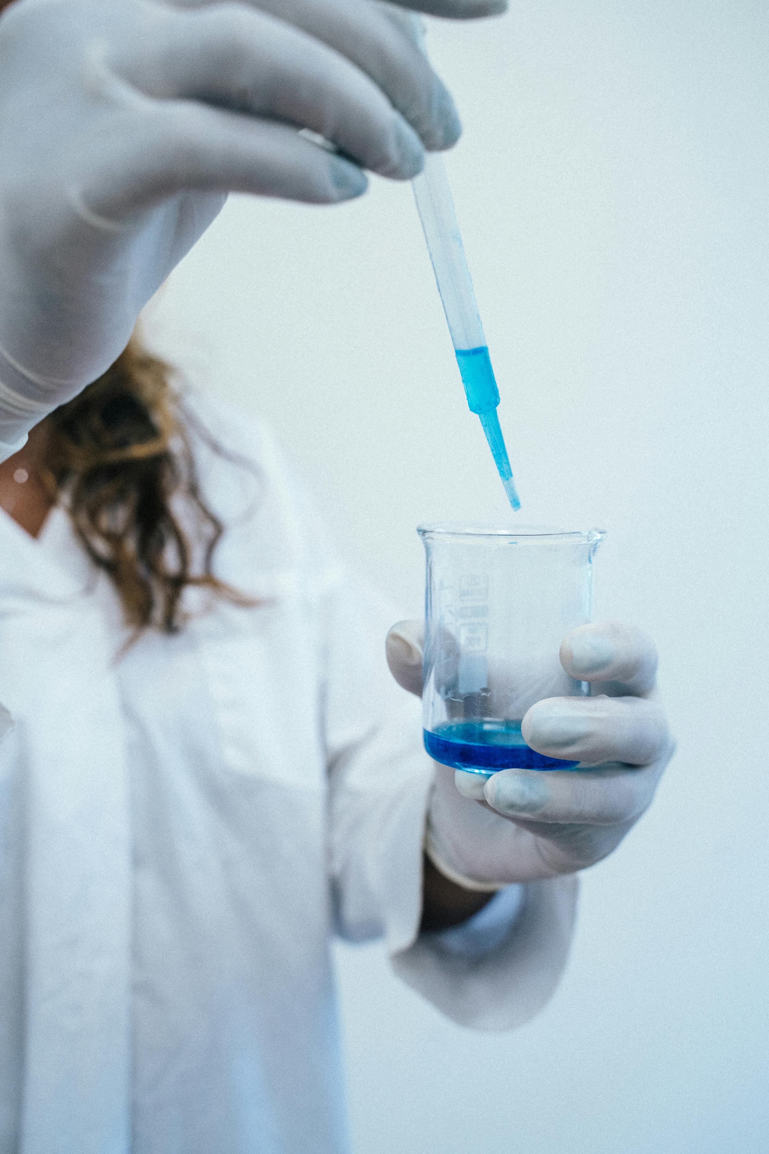 Person Holding a Dropper and Beaker With Blue Liquid · Free Stock Photo