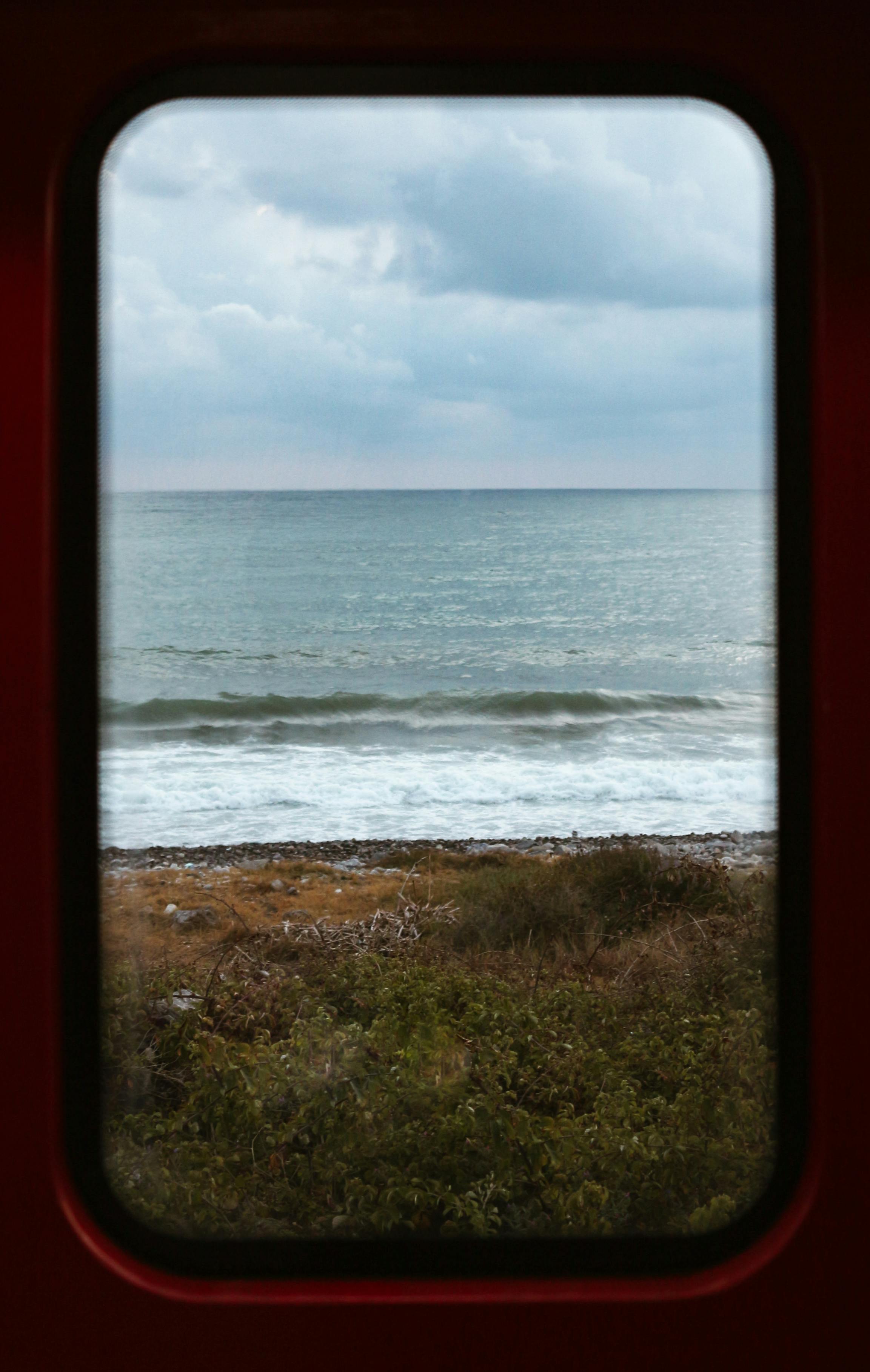 Train window against endless sea under cloudy sky · Free Stock Photo