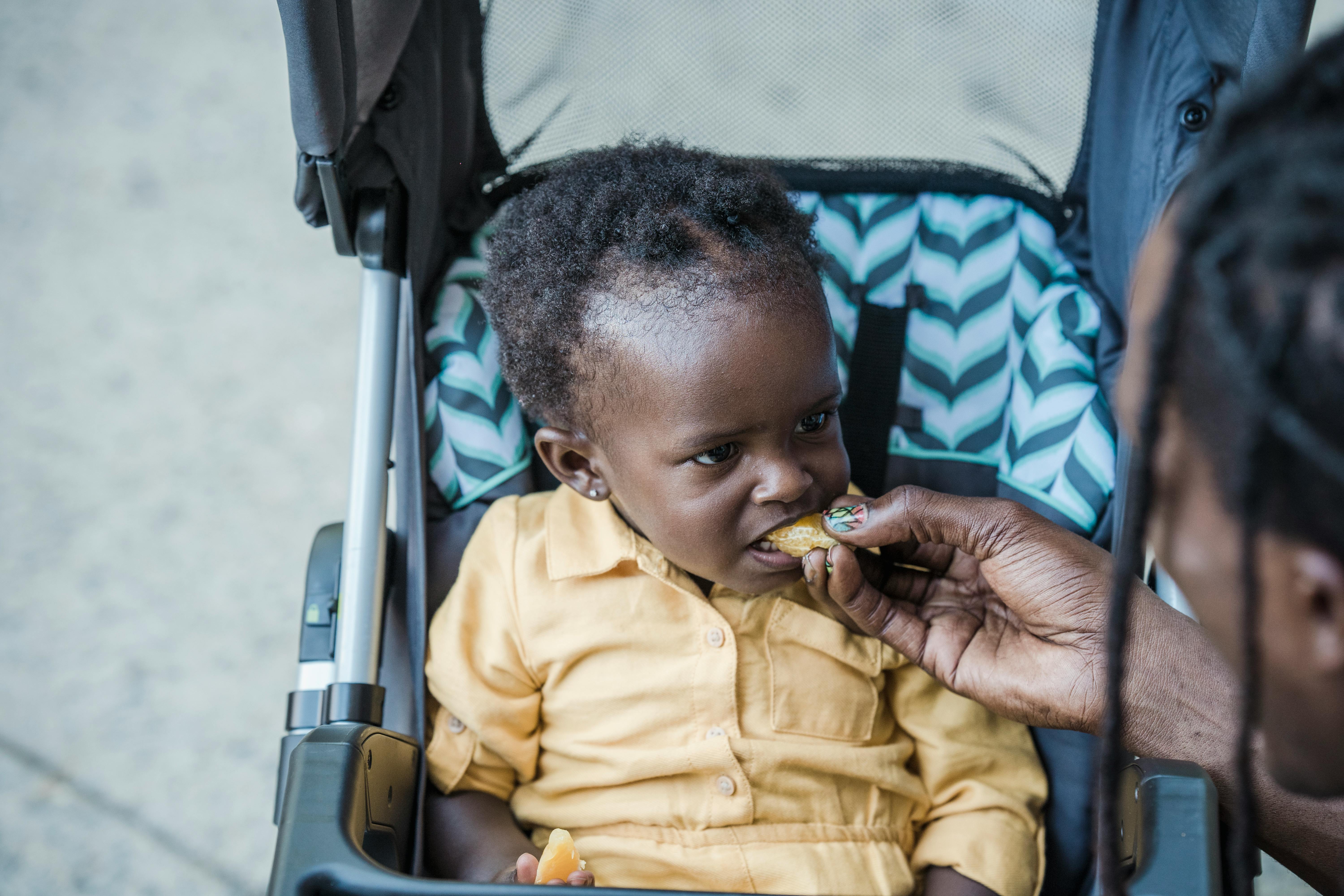Person Hand Feeding a Child Sitting on a Baby Stroller · Free Stock Photo