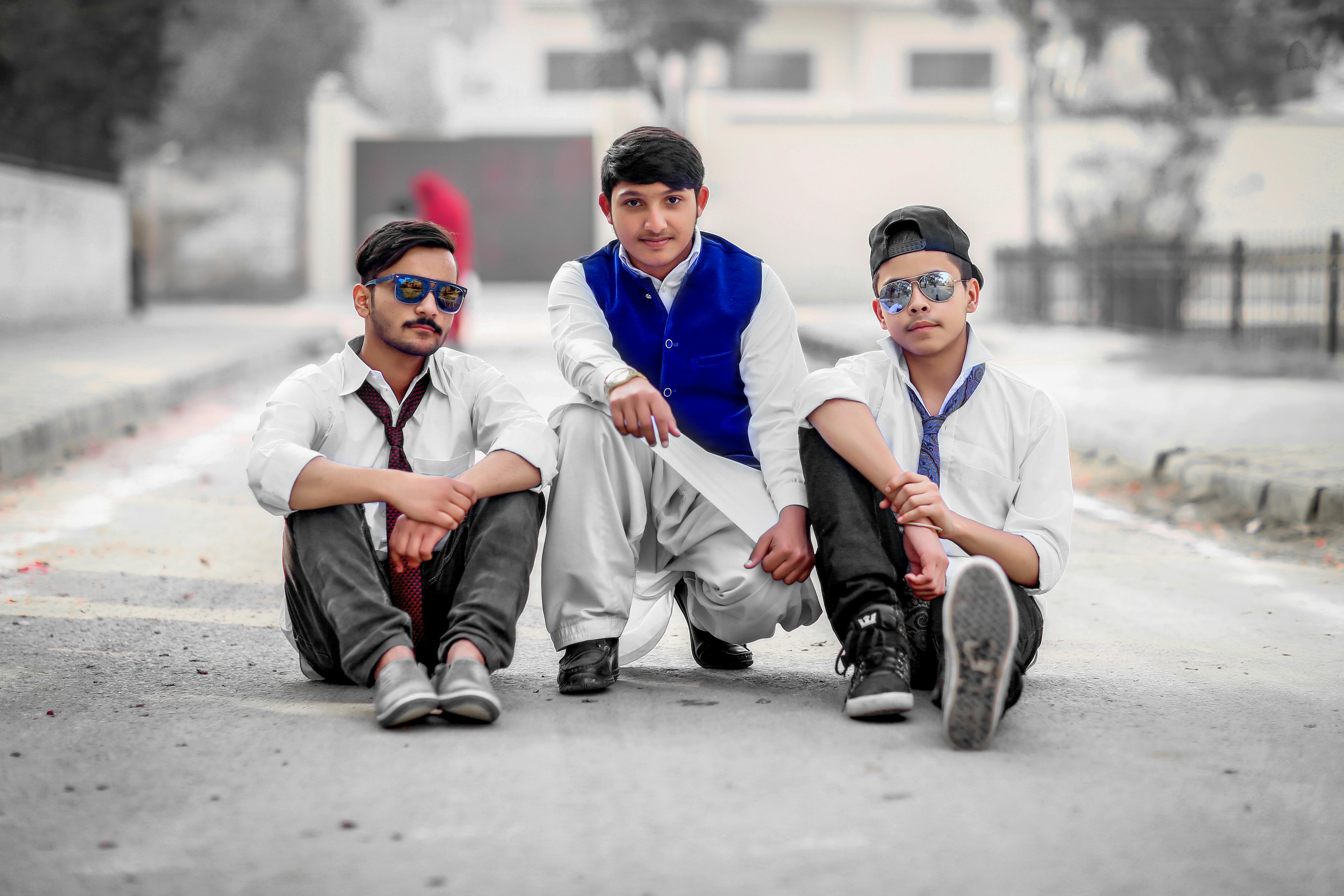 Three Men Sitting on Gray Concrete Road · Free Stock Photo