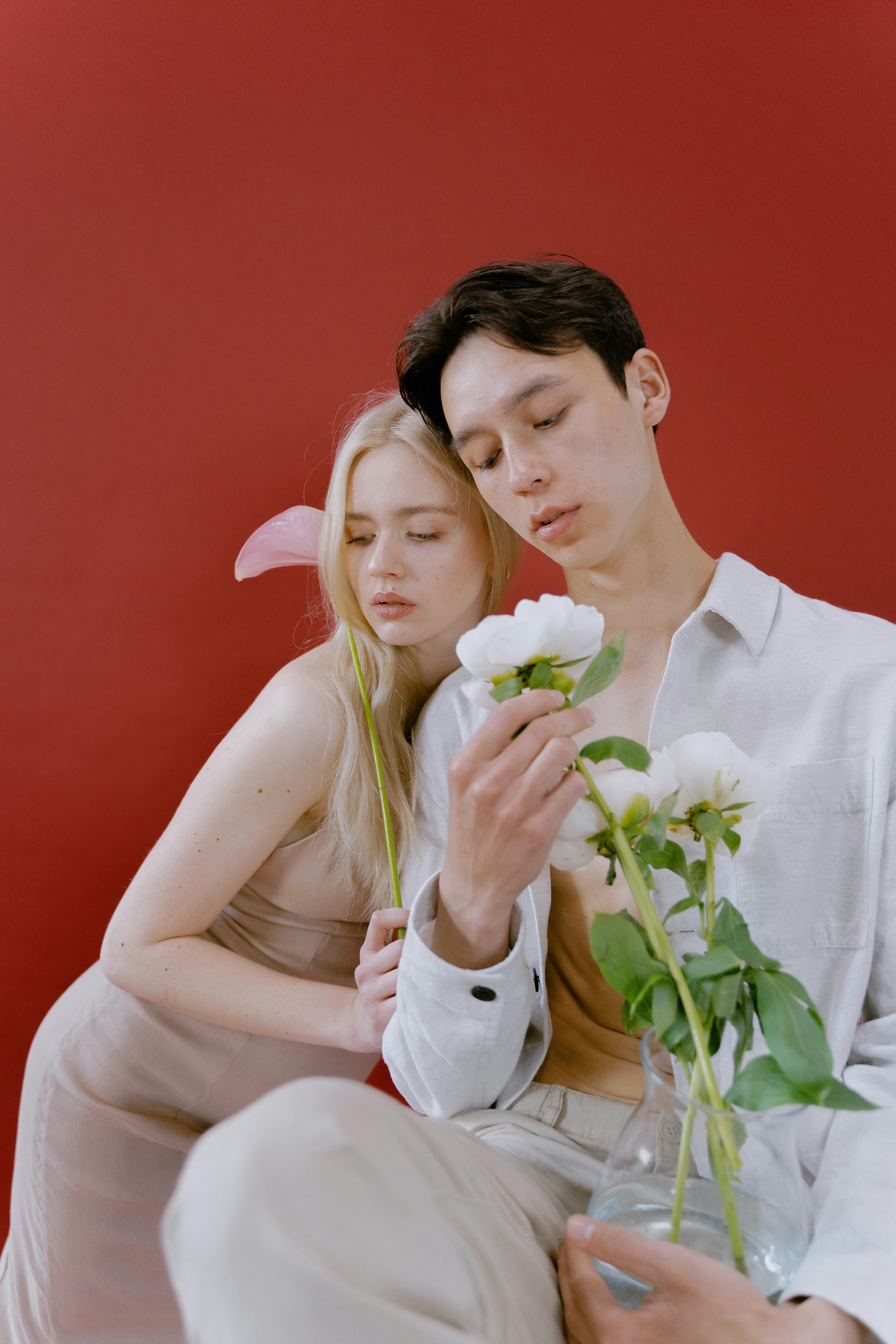 Romantic Couple Holding Flowers on Red Background · Free Stock Photo