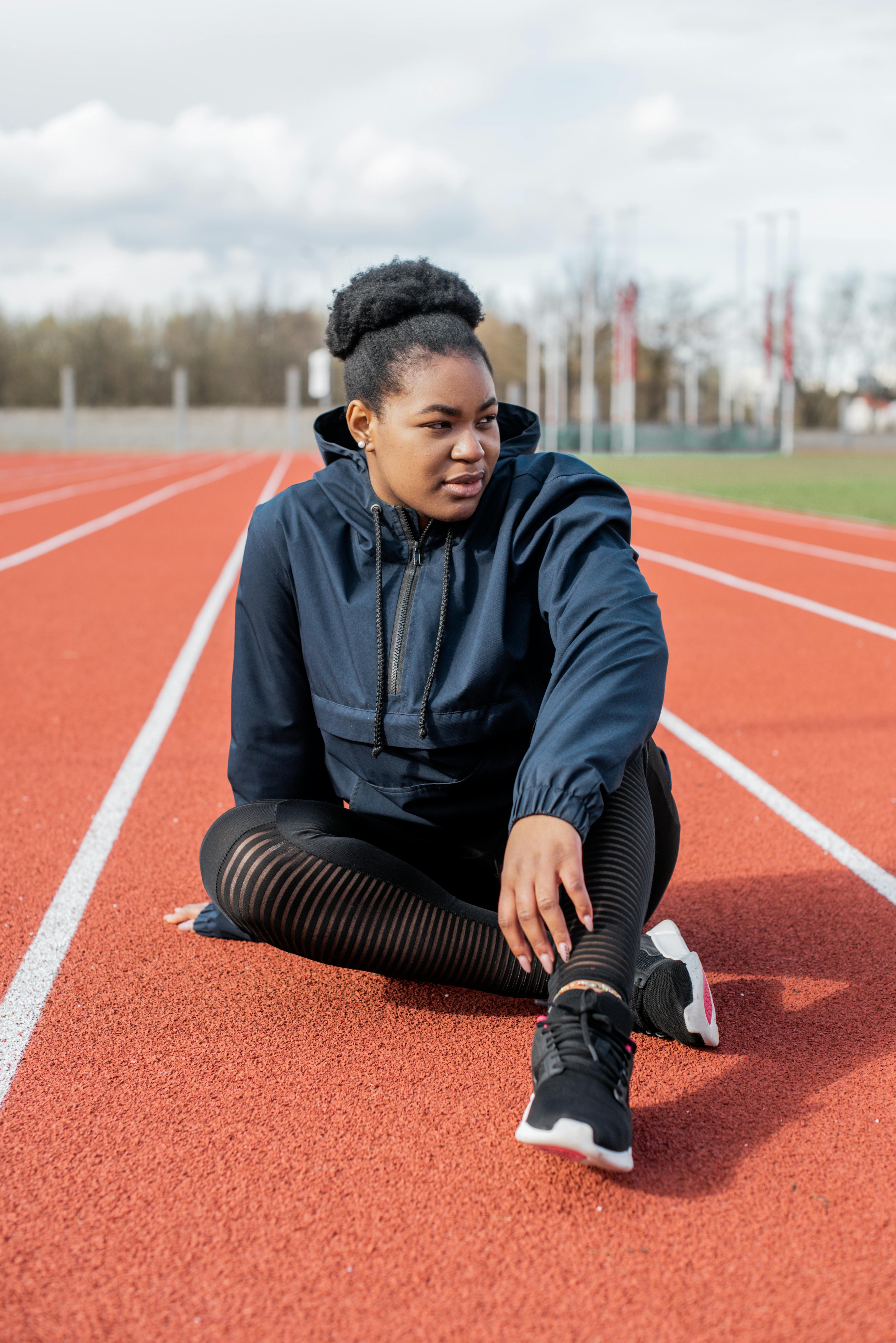 Woman in Blue Jacket Sitting on Running Track · Free Stock Photo