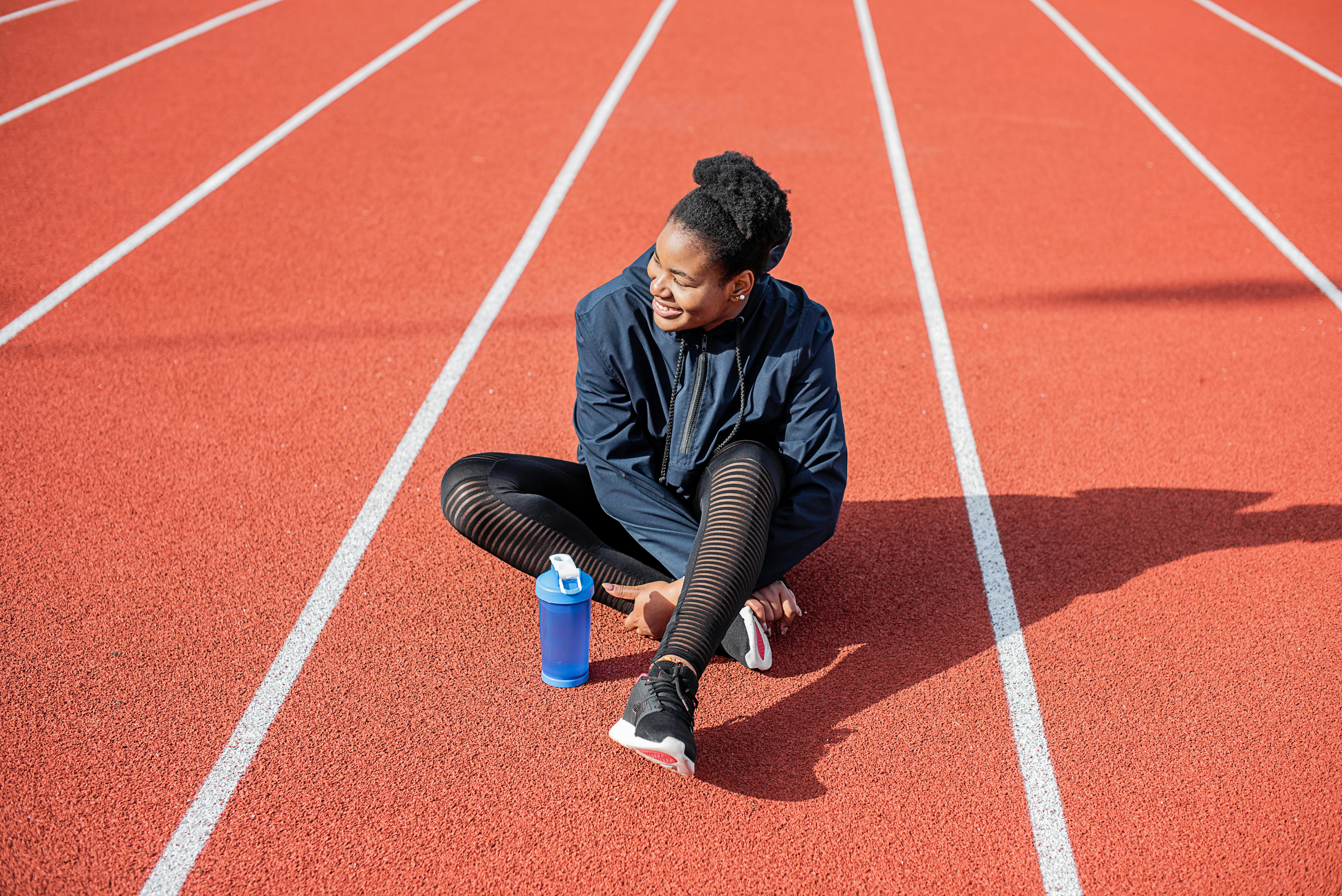 Woman in Blue Jacket Sitting on Running Track · Free Stock Photo