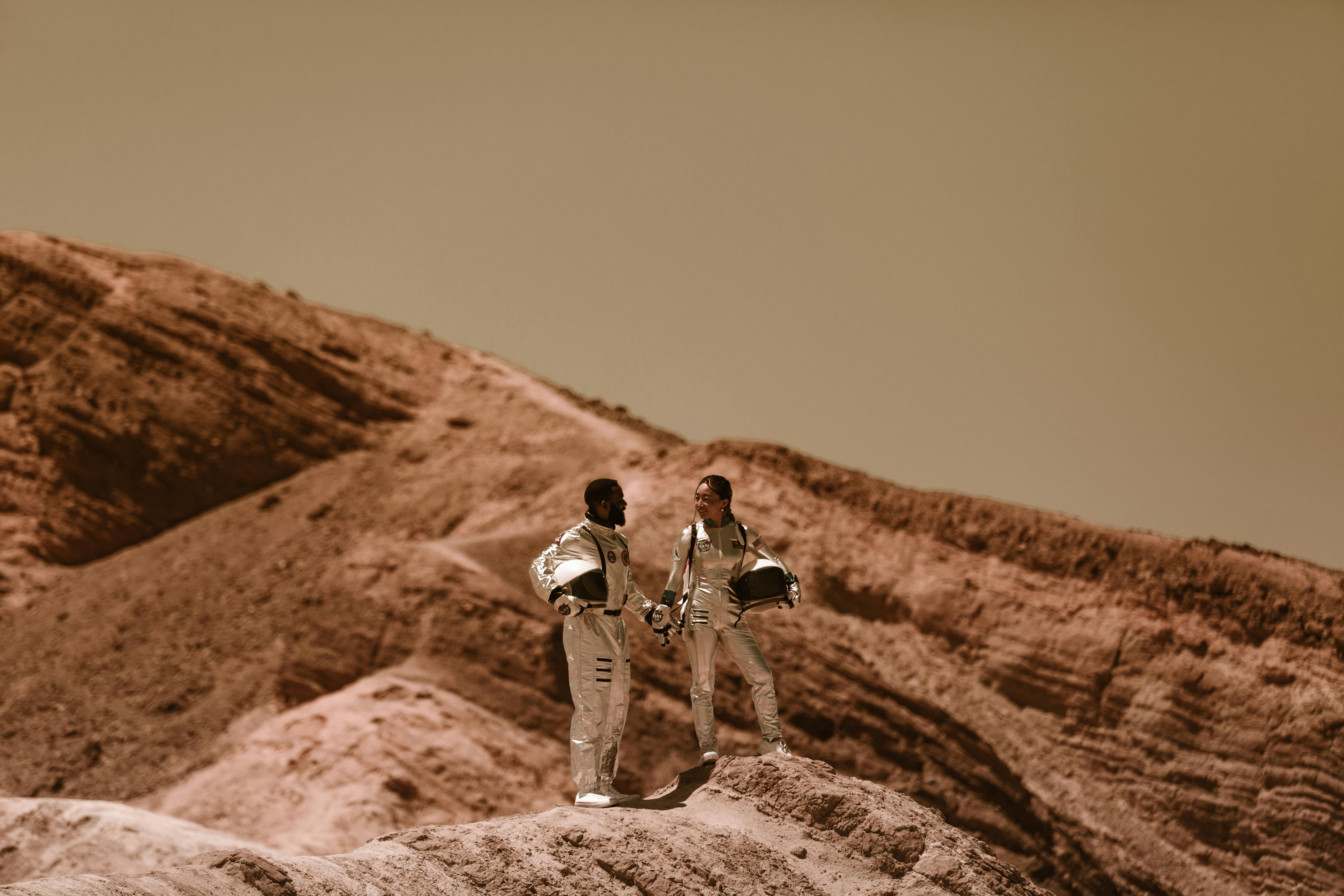 A Couple in Space Suit Standing on a Rock Formations while Holding ...