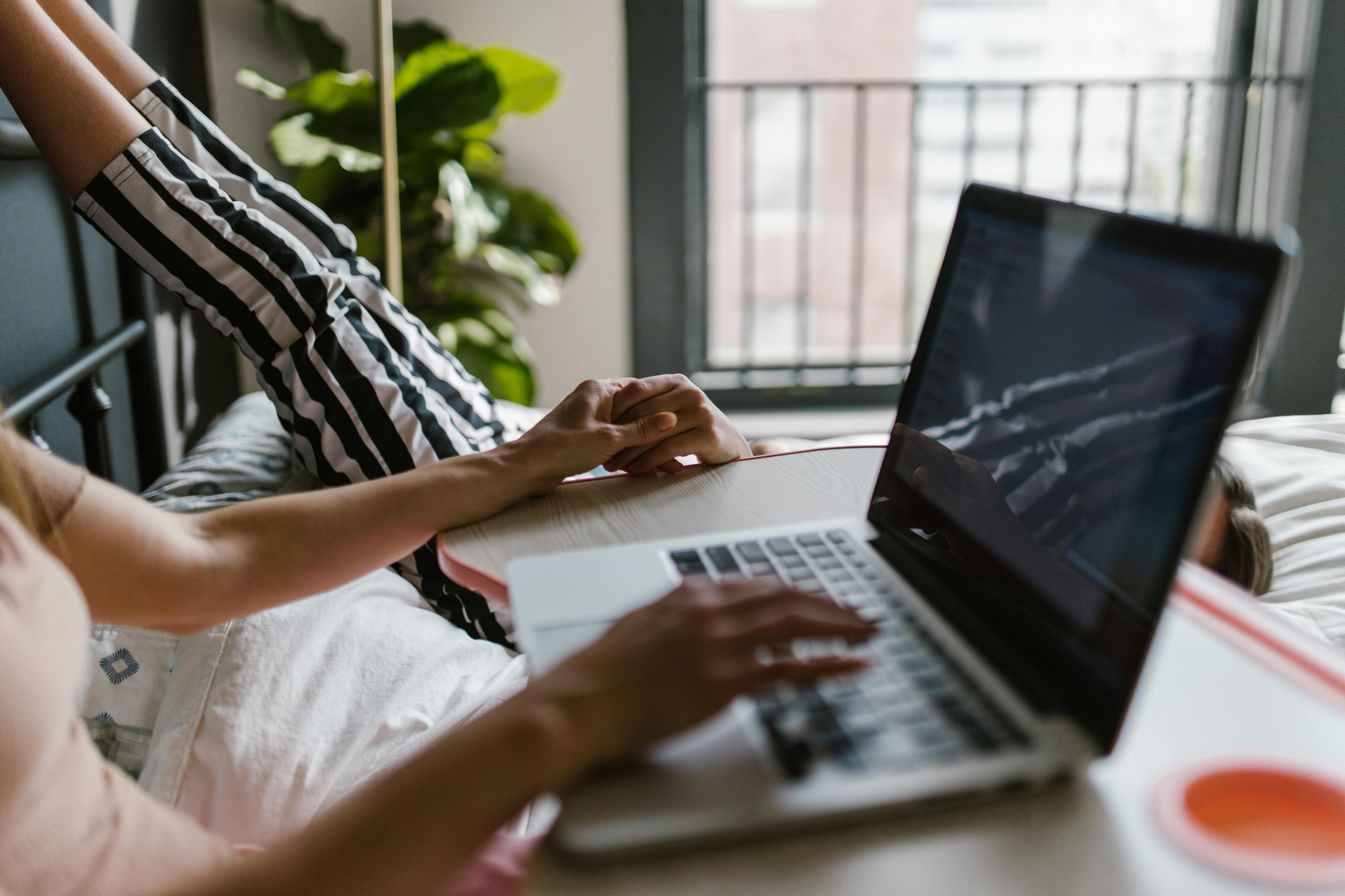 Holding Hands while Working on Laptop in Bed · Free Stock Photo