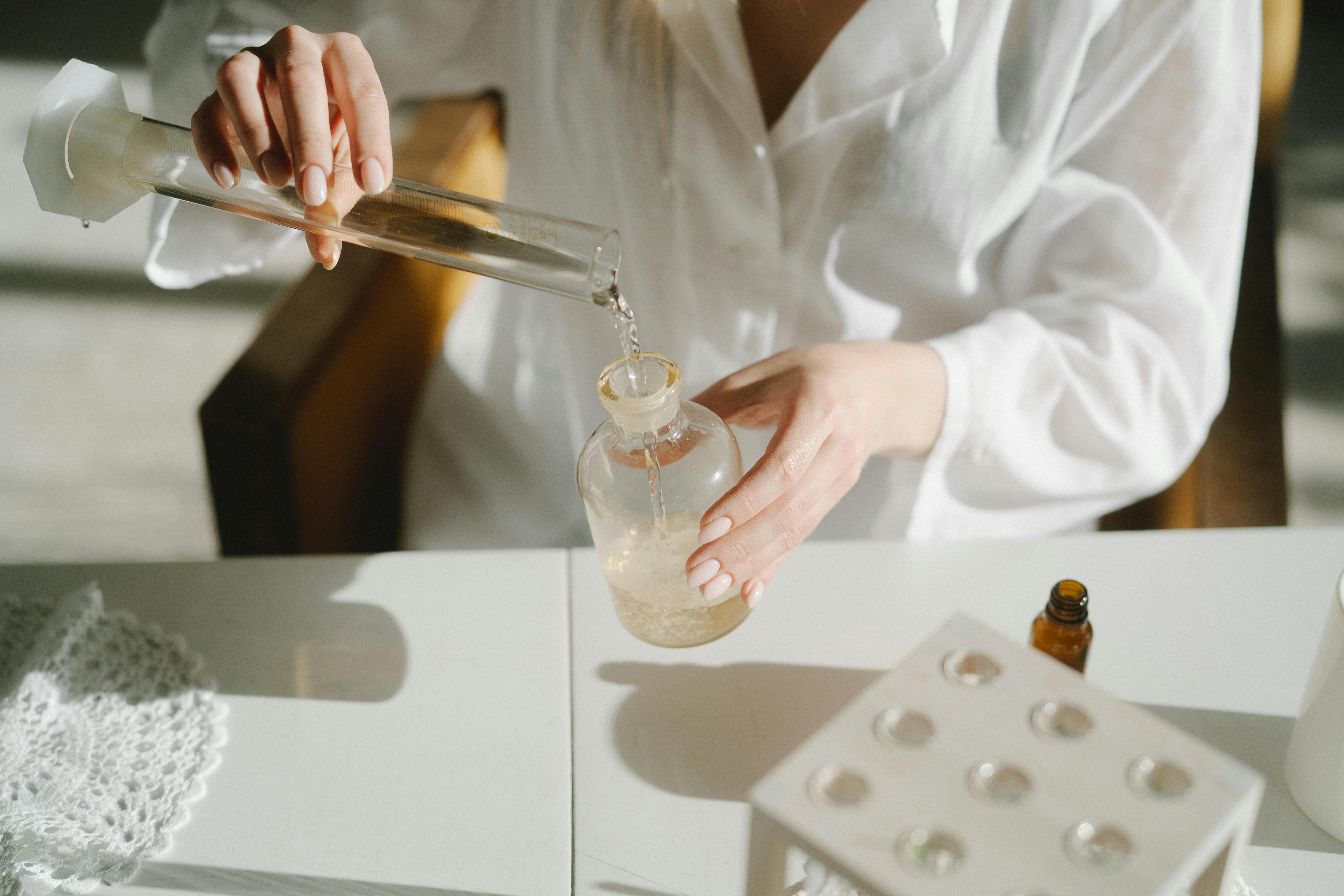 Person in White Long Sleeves Transferring Water on Clear Glass Bottle ...
