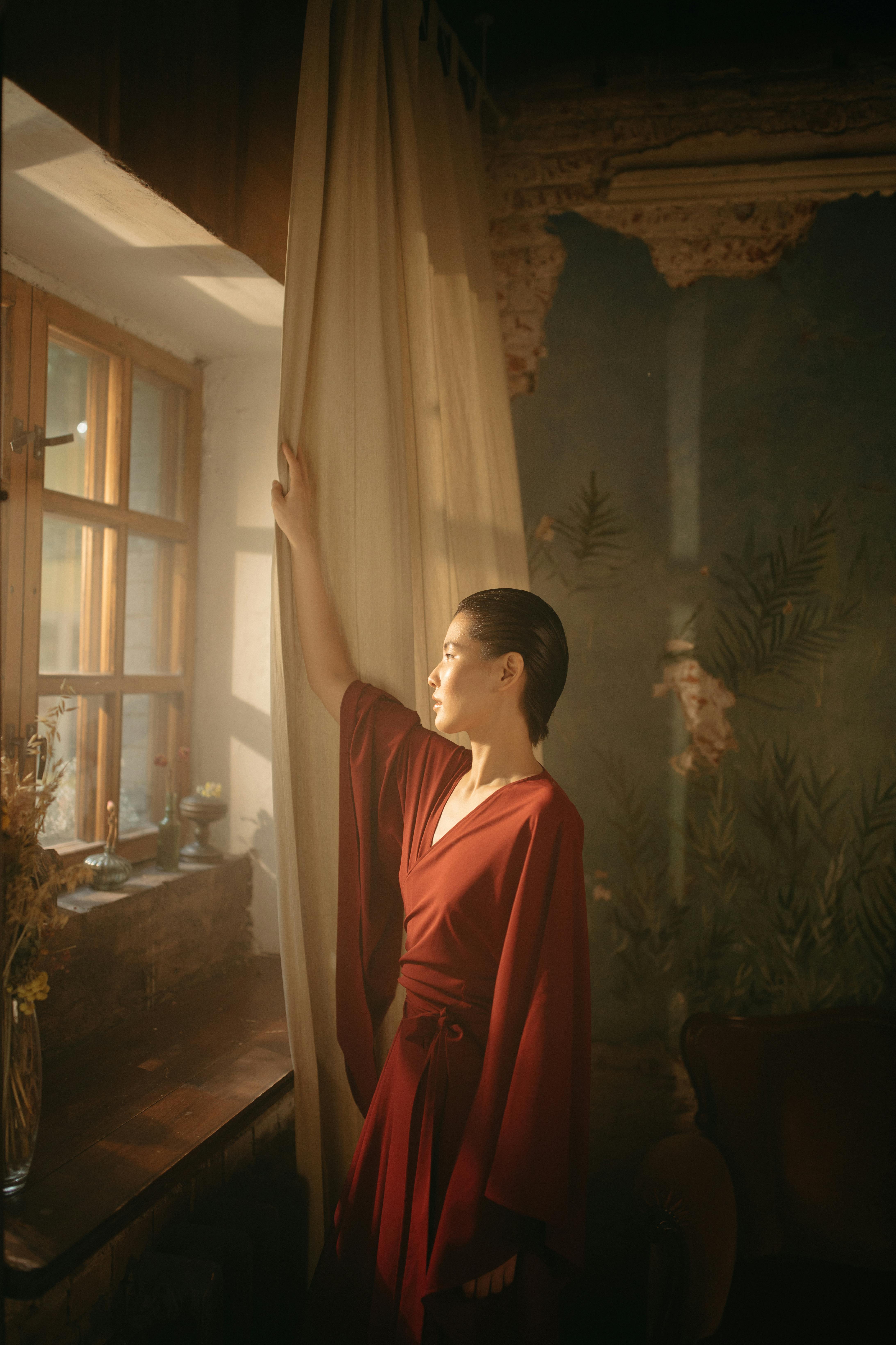 Woman in Red Robe Holding Curtain · Free Stock Photo