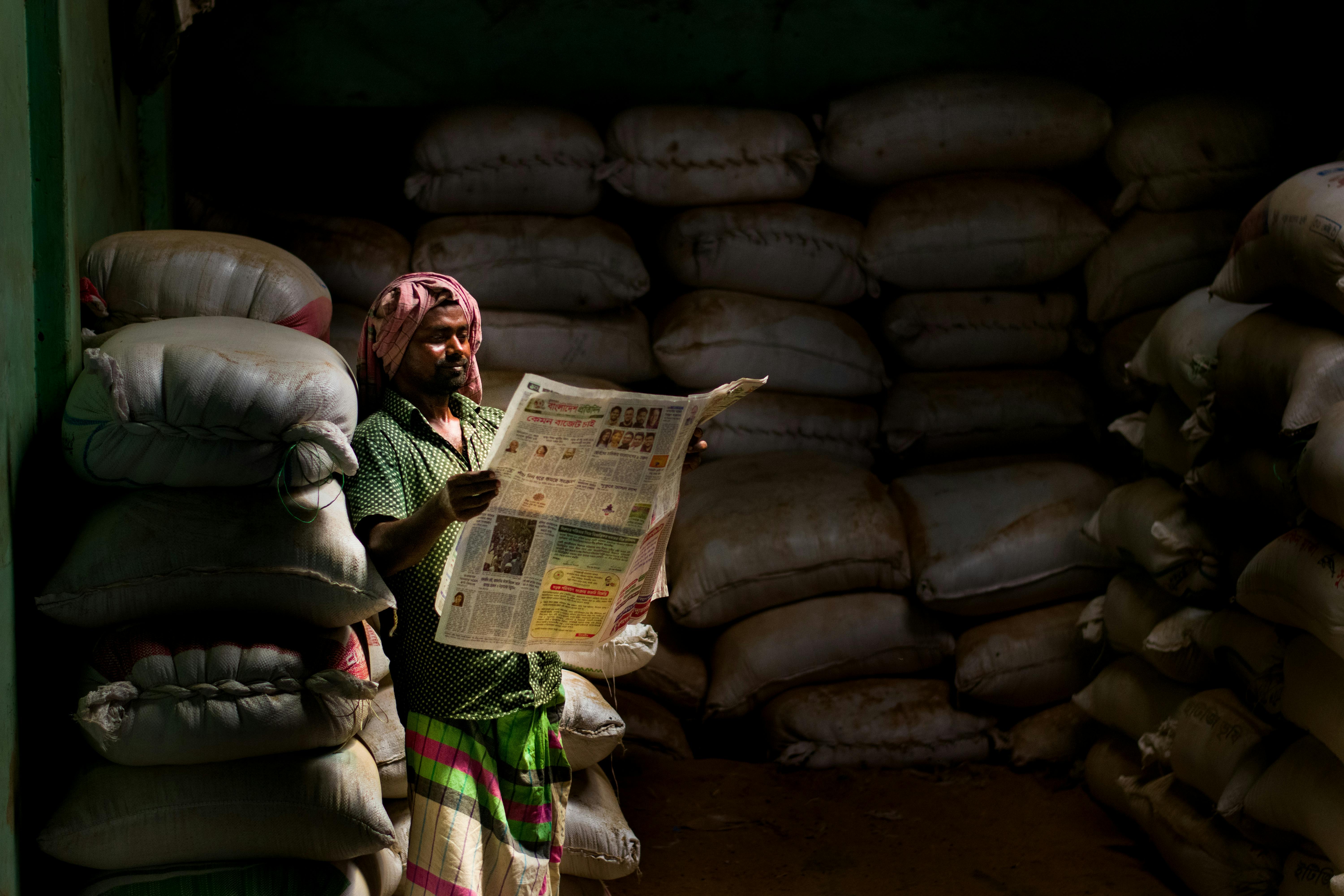 Man Reading Newspaper inside a Storeroom with Stack of Sacks · Free ...