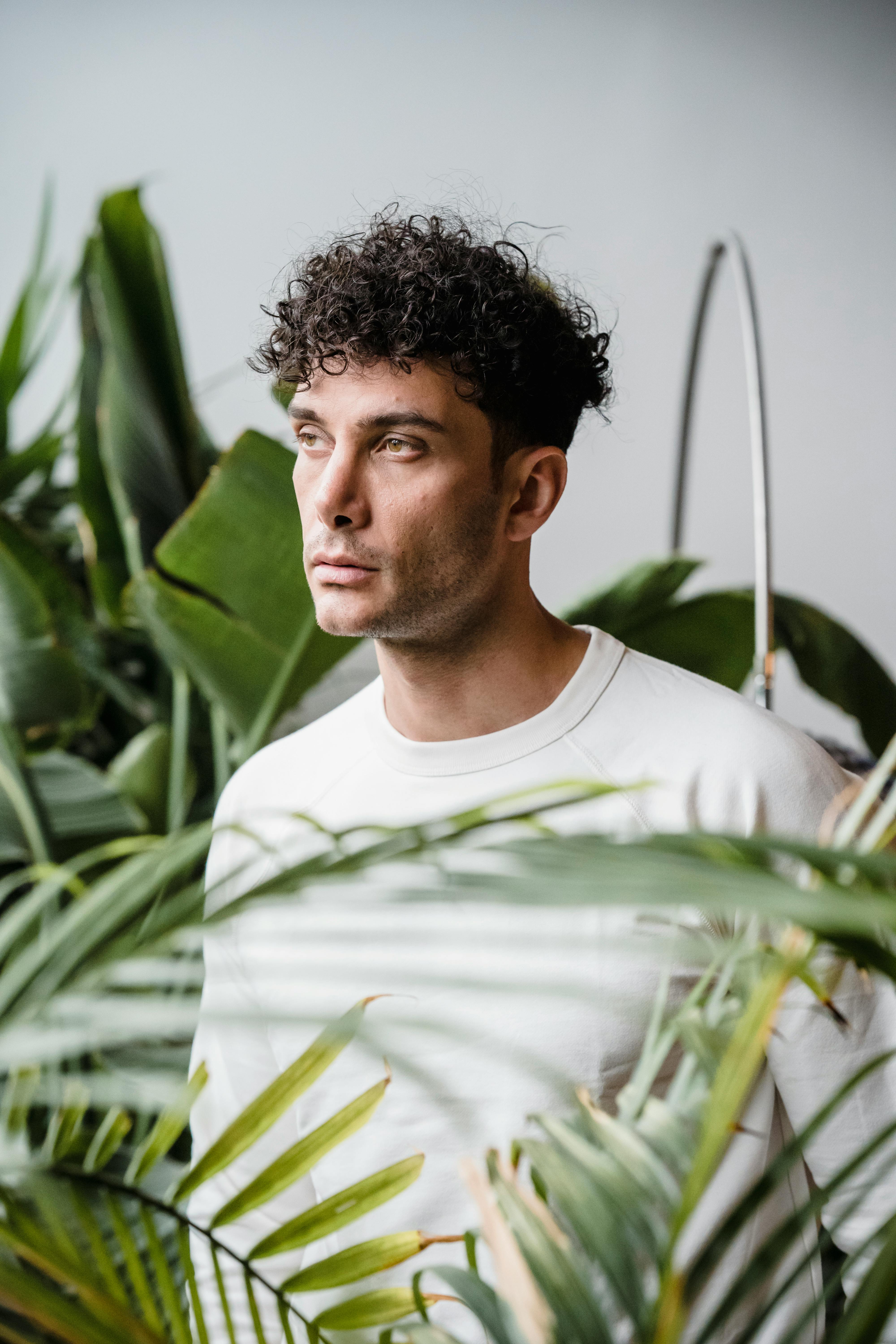 A Sad Man in White Long Sleeves Shirt Standing Near Green Plants while ...