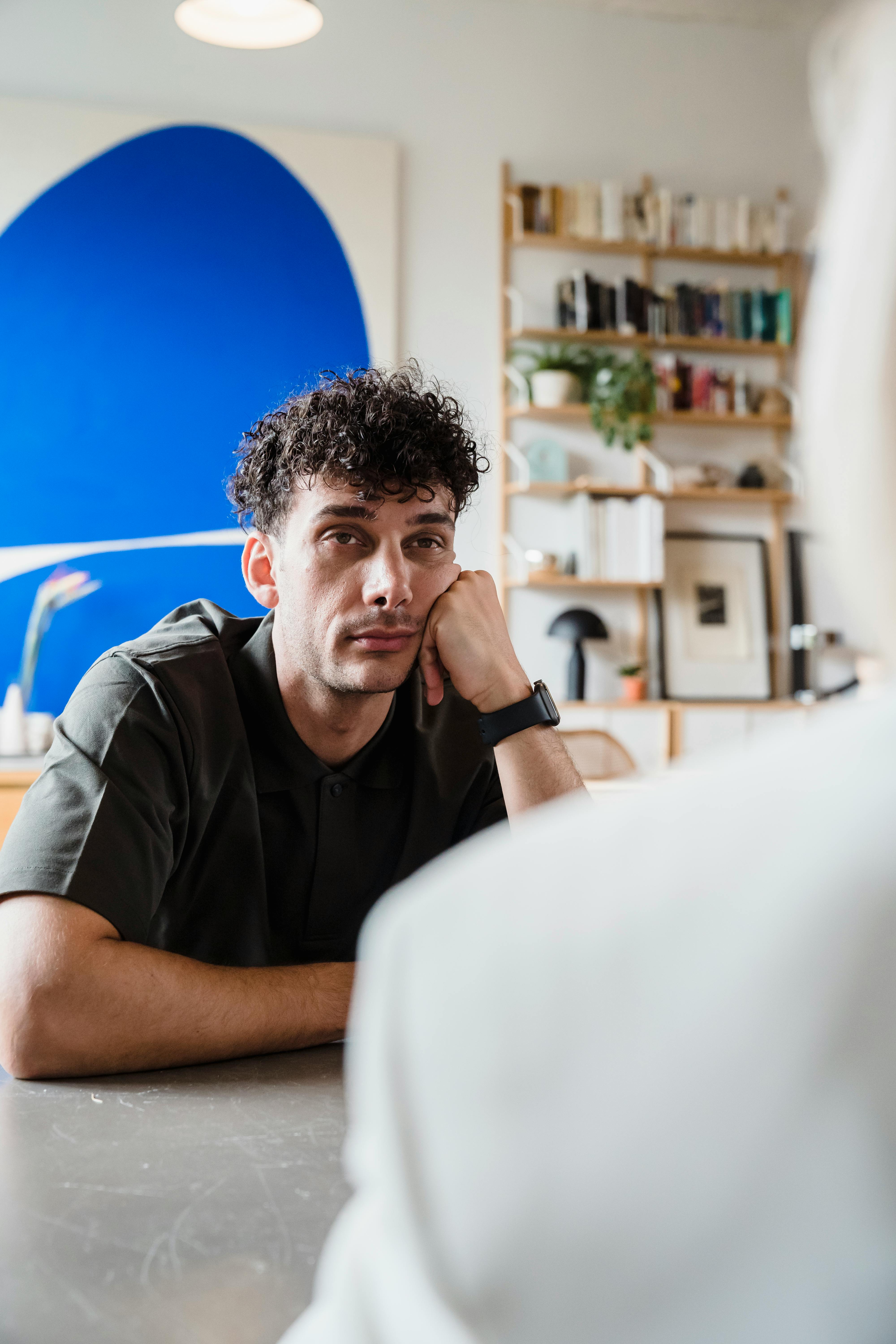 Sleepy Man Sitting with Hand on Cheek · Free Stock Photo
