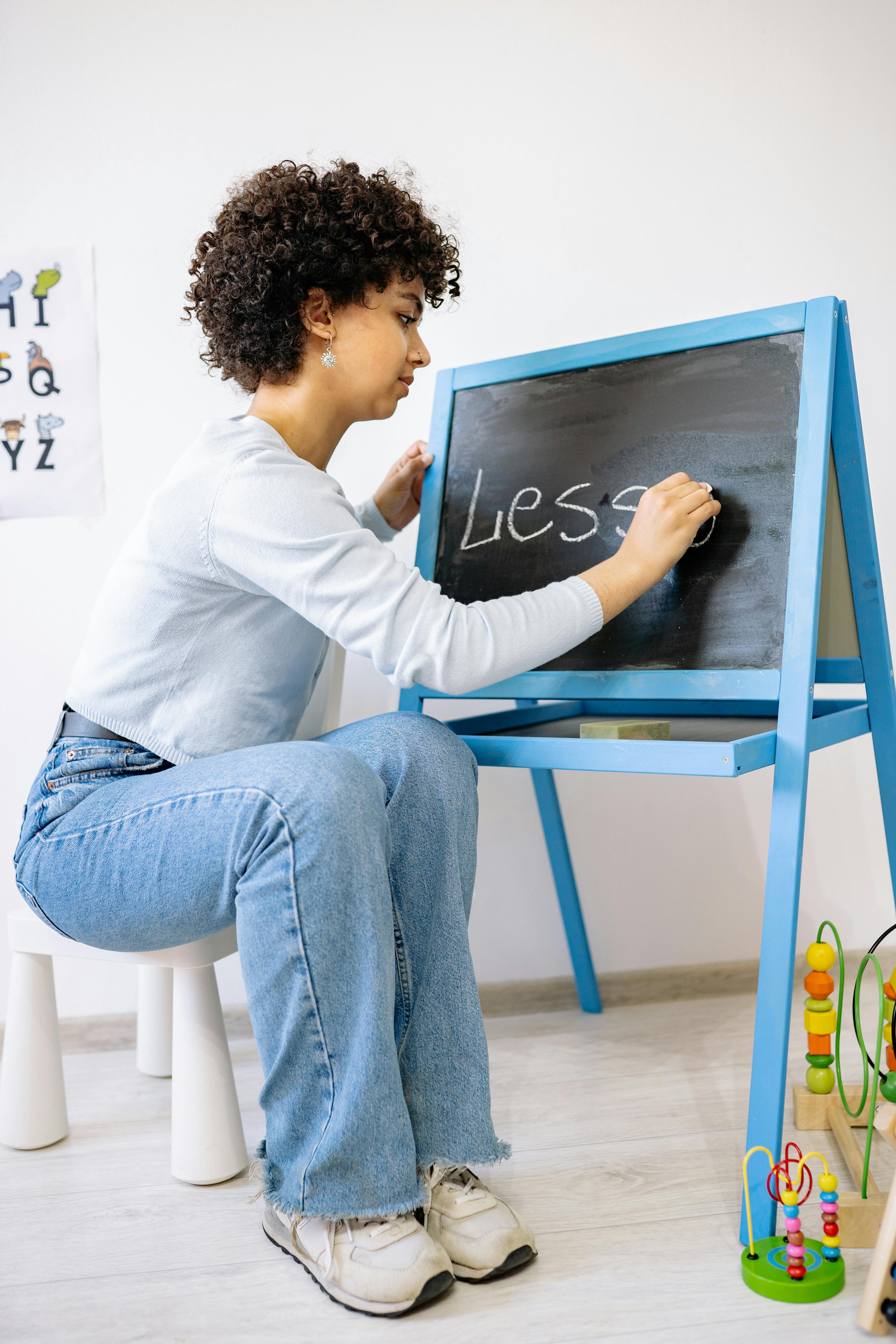 Woman in White Dress Shirt and Blue Denim Jeans Writing On Blackboard ...