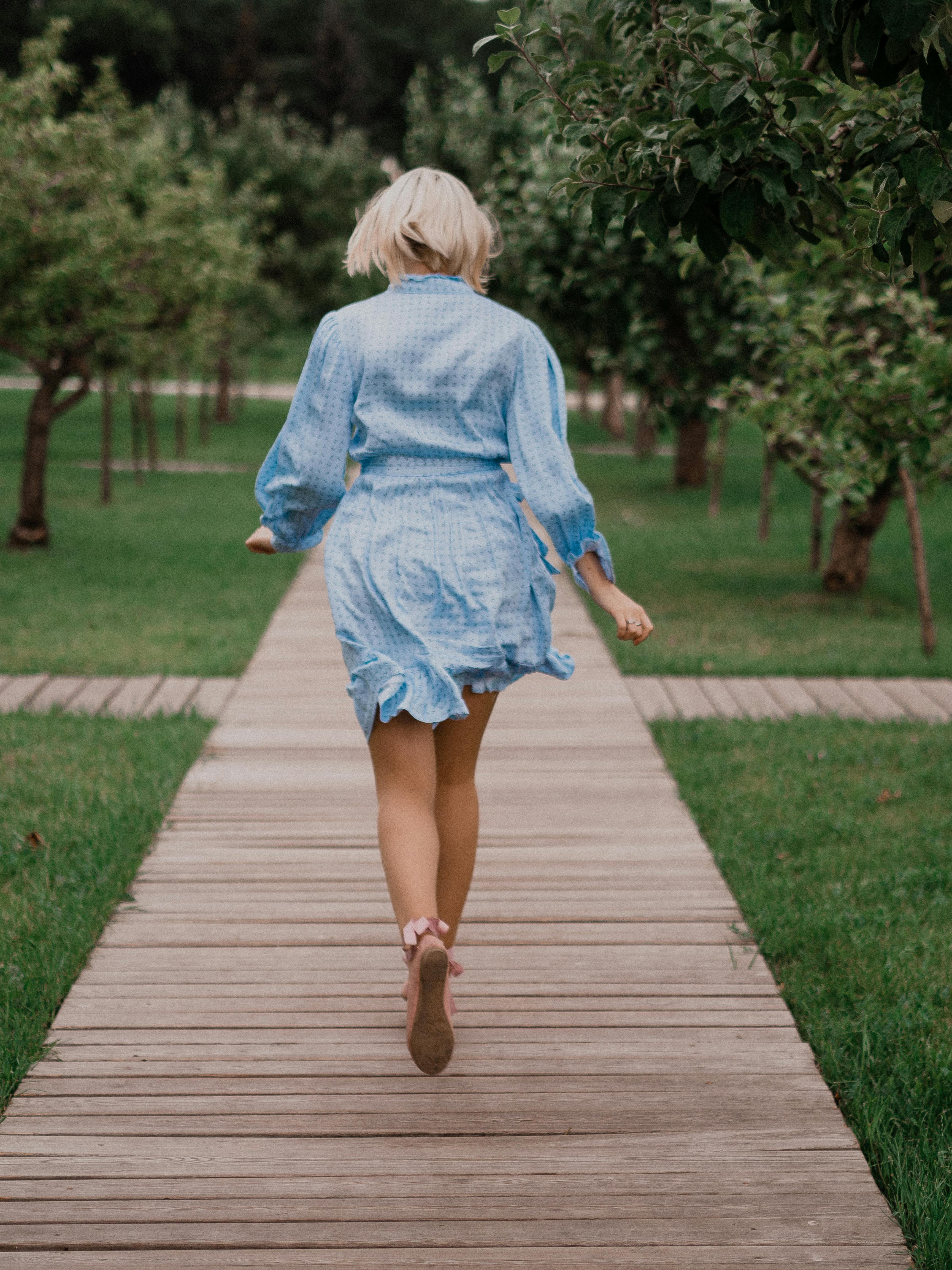 Woman in Blue Dress Running on Wooden Pathway · Free Stock Photo