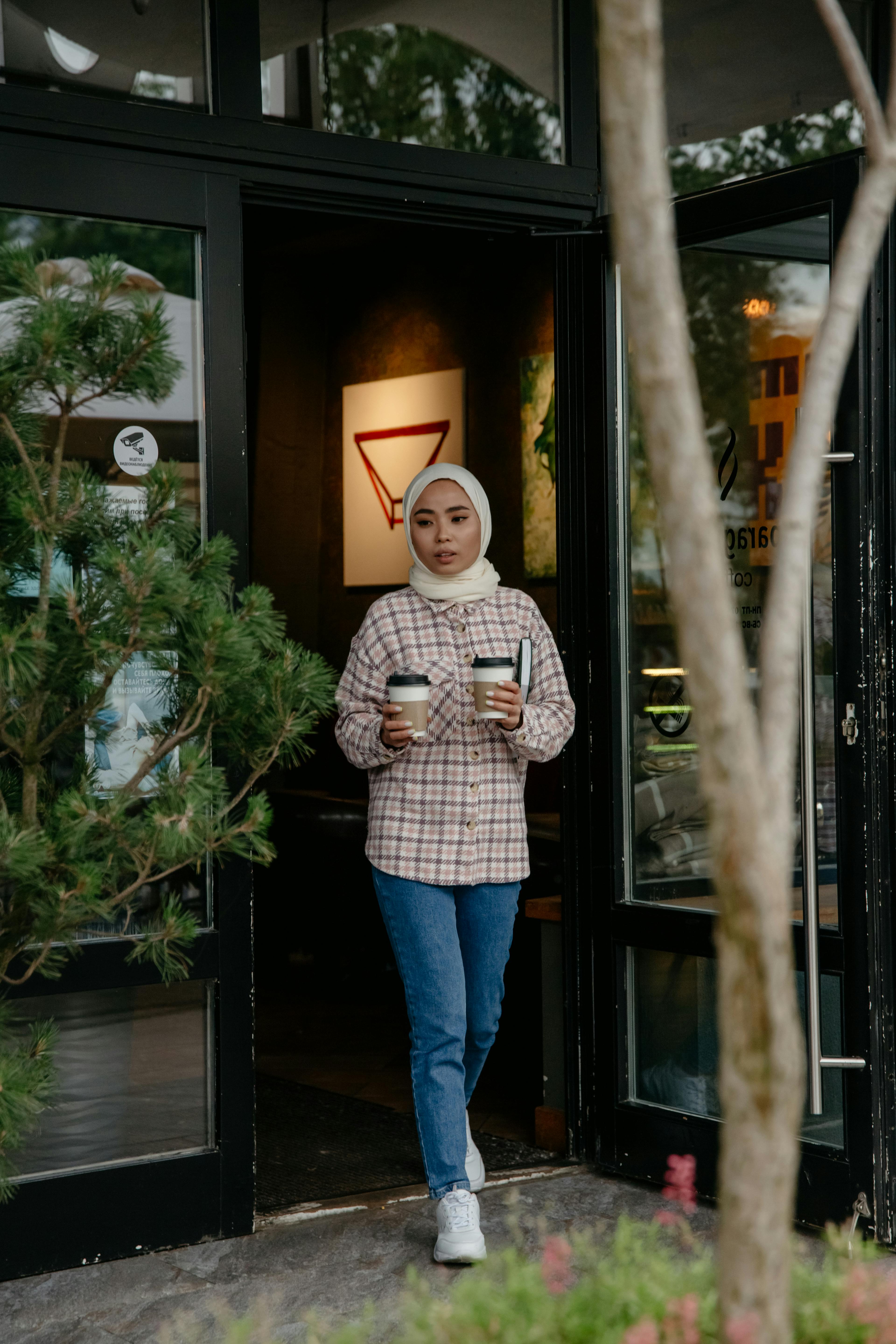 Young Woman in a White Hijab Leaves a Cafe Carrying Two Coffees · Free ...