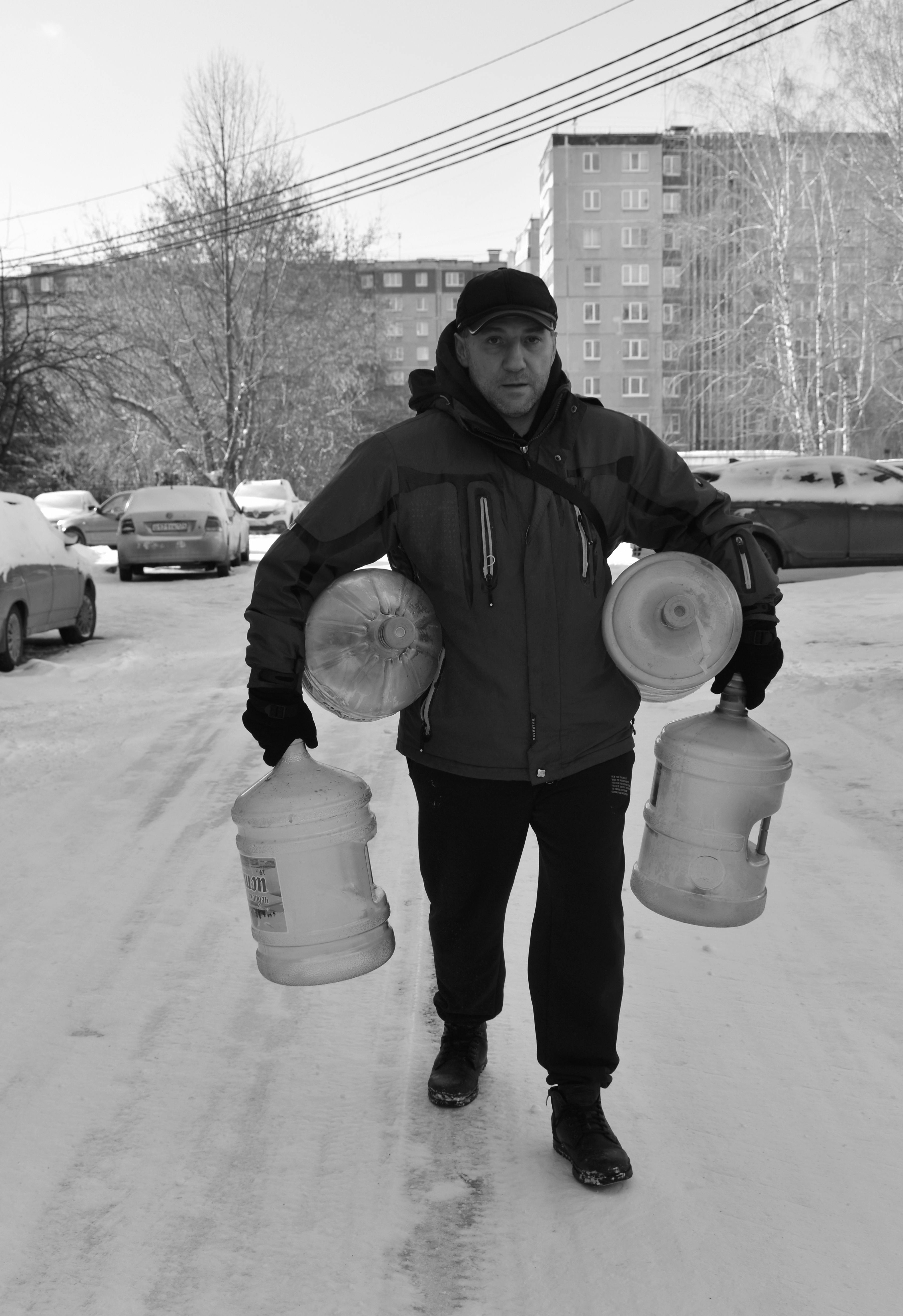 Grayscale Photo of a Man Carrying Water Containers · Free Stock Photo