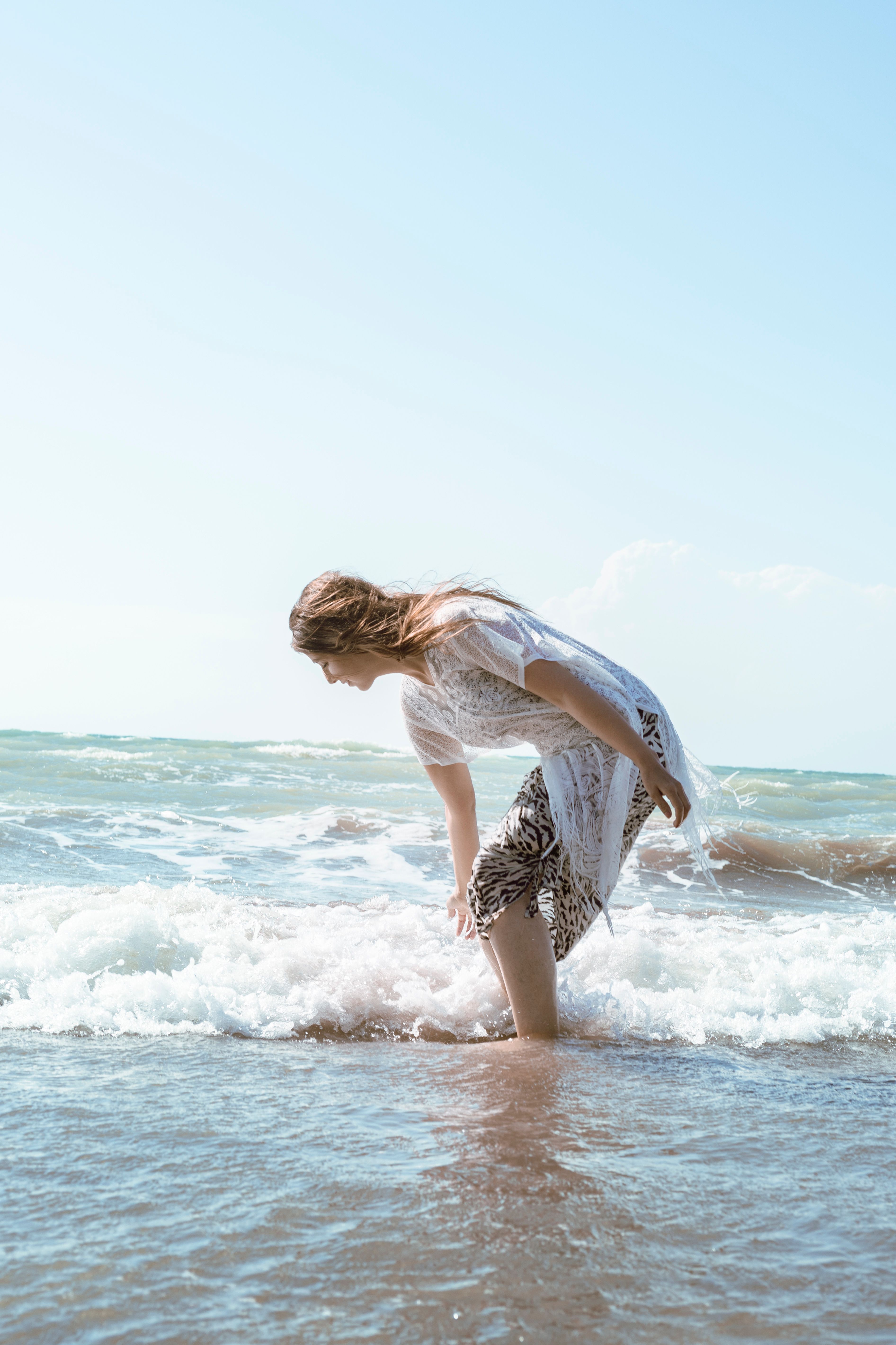 A Woman in White Dress Touching Waves on the Beach · Free Stock Photo