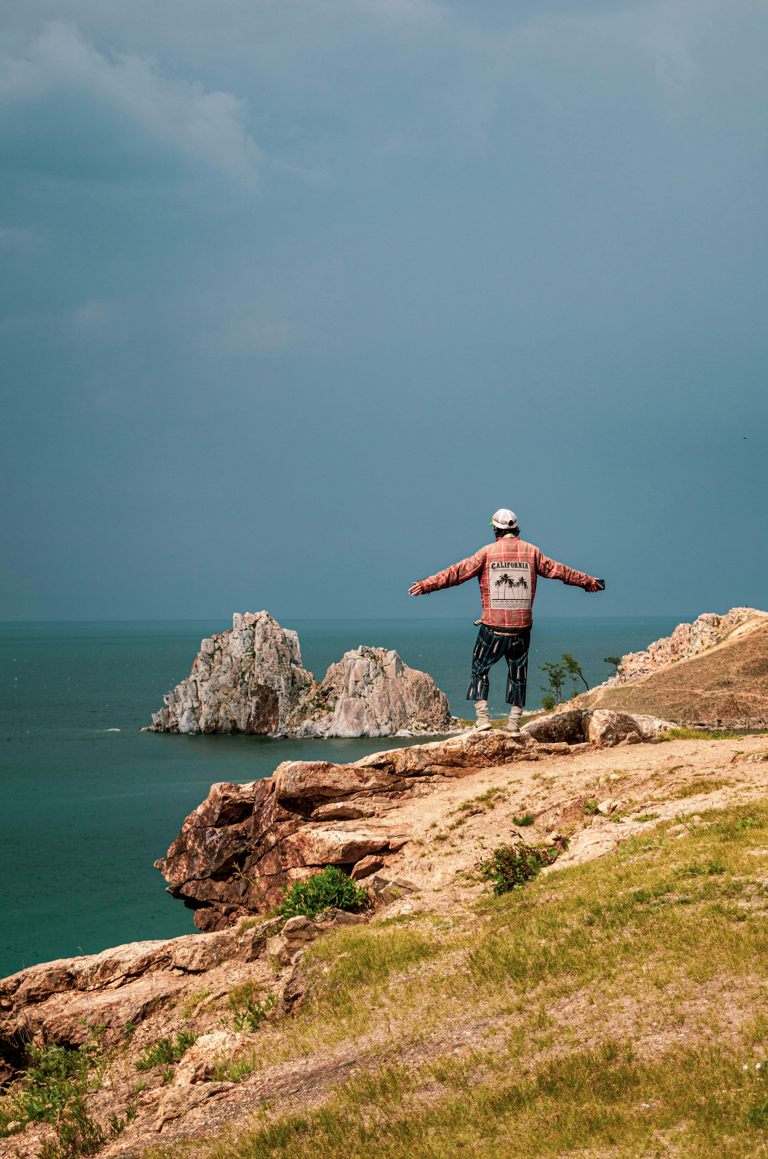 Man Sitting between Stones Heaps on Hill on Sea Shore · Free Stock Photo