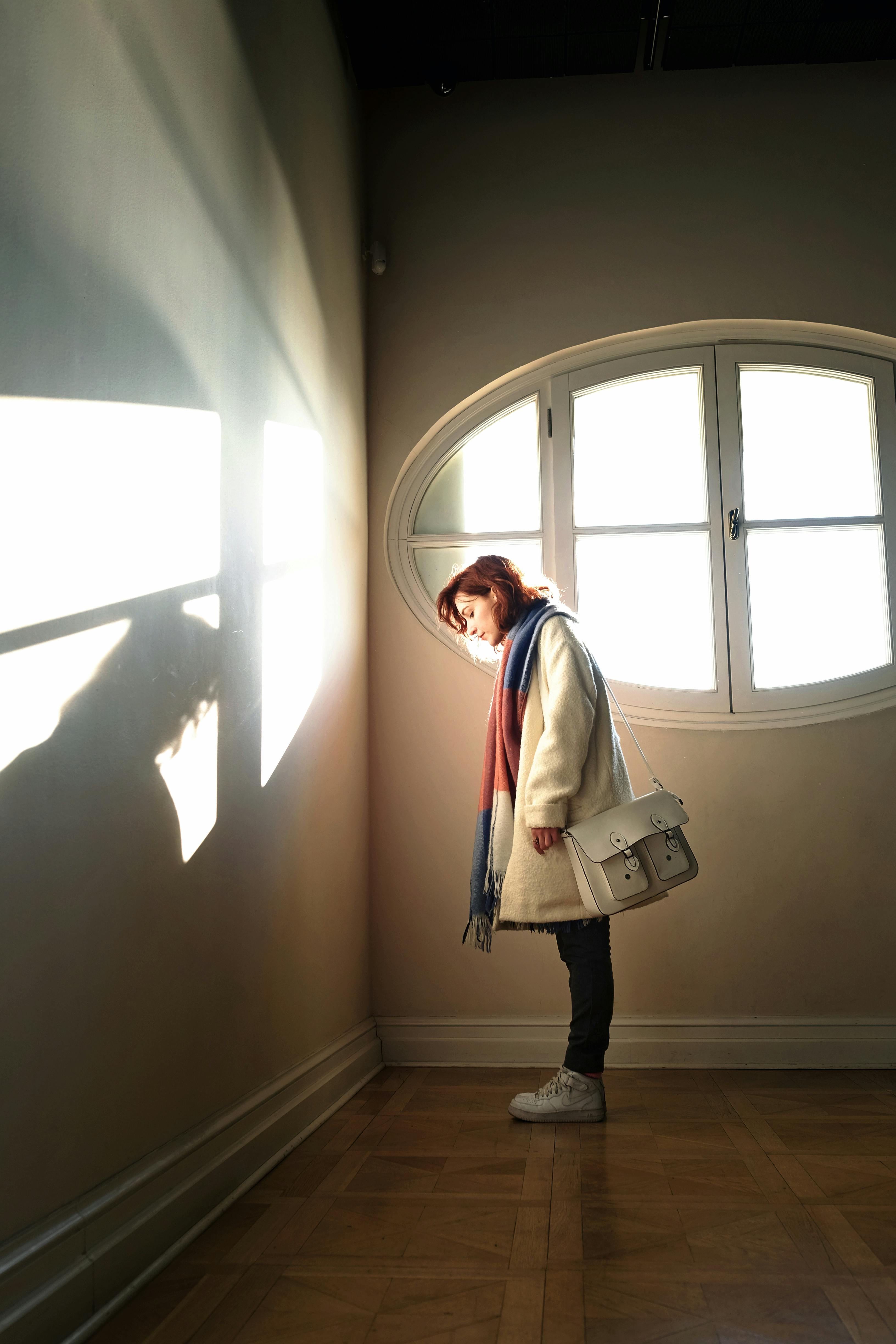 Woman Standing in a Building Next to an Ellipse Window · Free Stock Photo